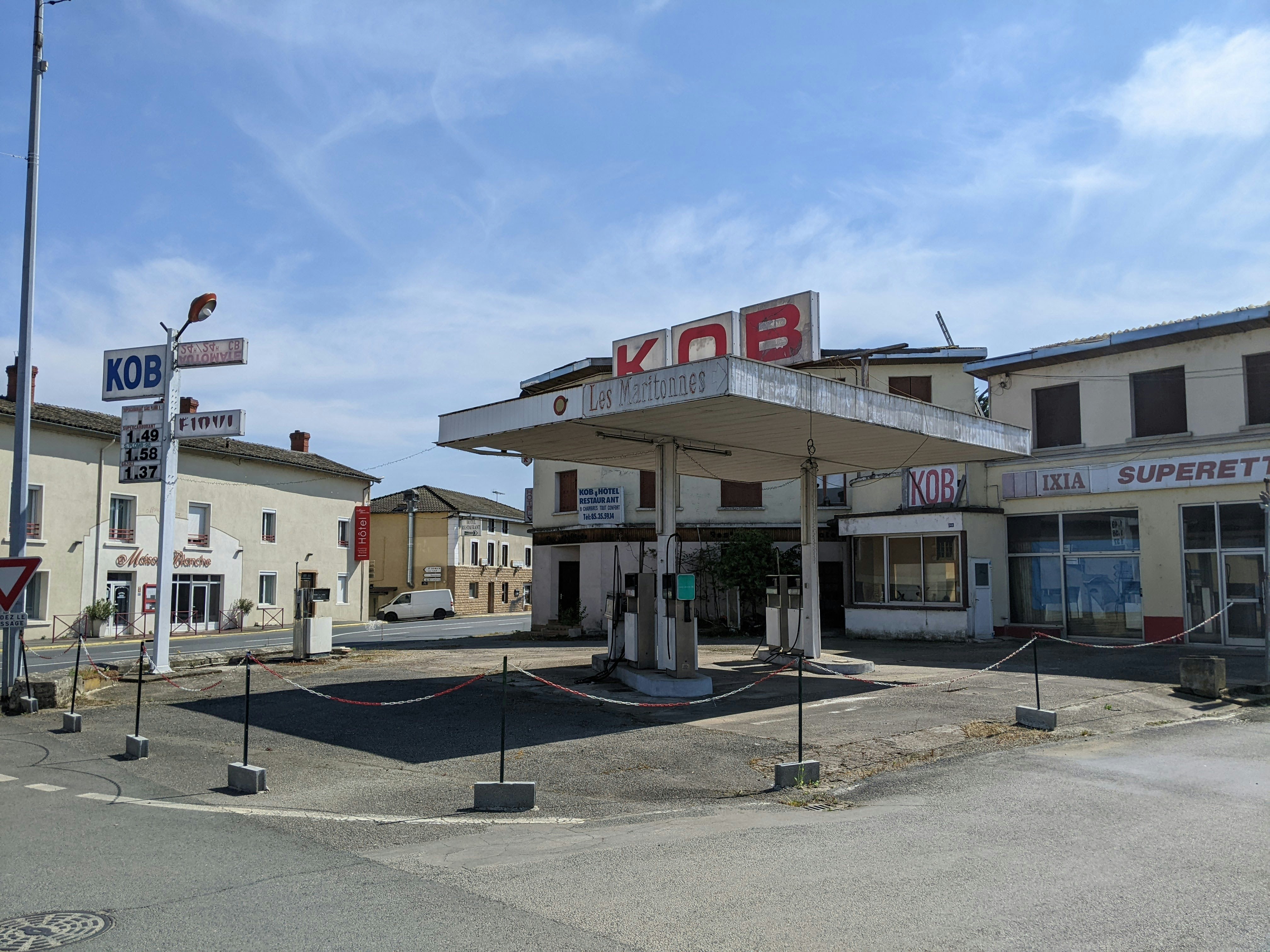 Abandoned gas station with retro signage and surrounding buildings, showcasing a nostalgic atmosphere. The scene captures the essence of a forgotten roadside stop.