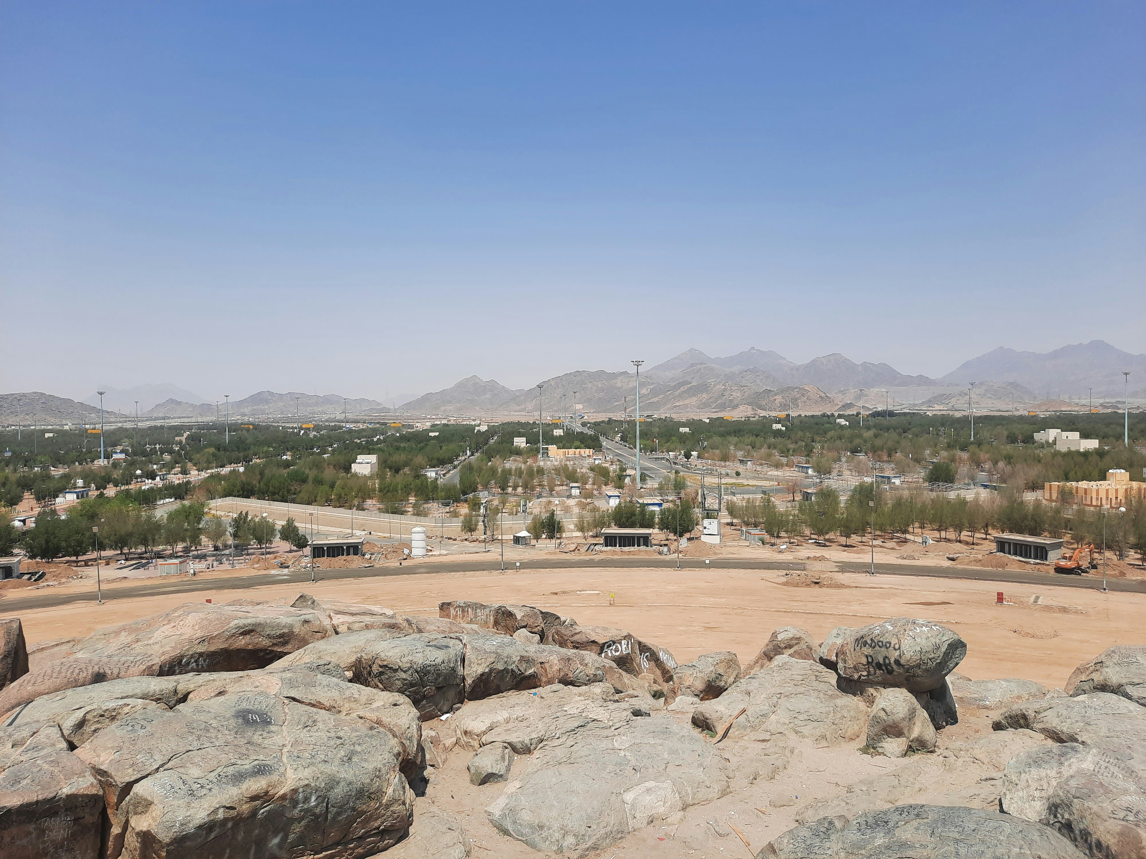 Rocky foreground with a sprawling cityscape and distant mountains under a clear blue sky.