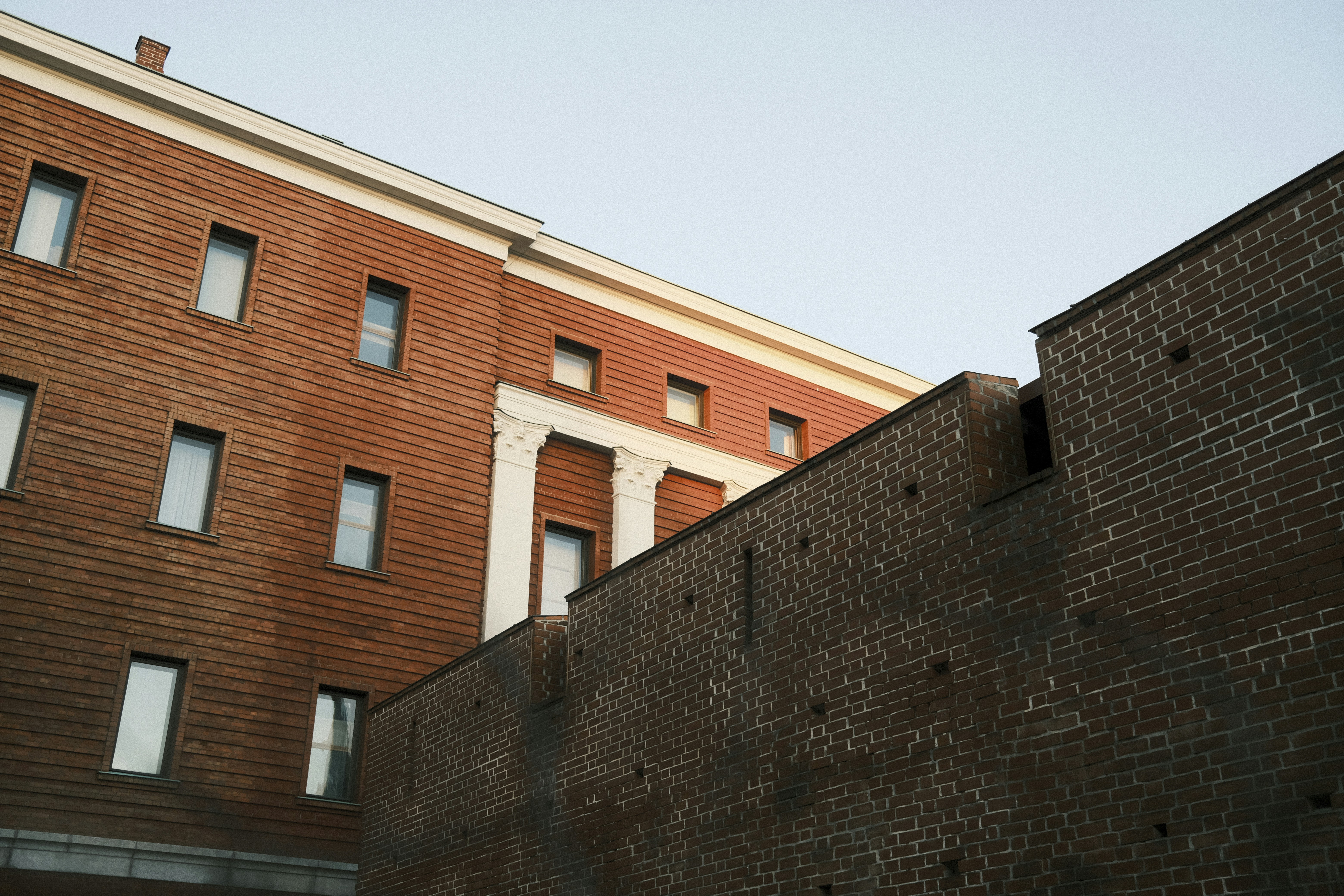 Brick building facade with rectangular windows and contrasting architectural elements against a clear sky.