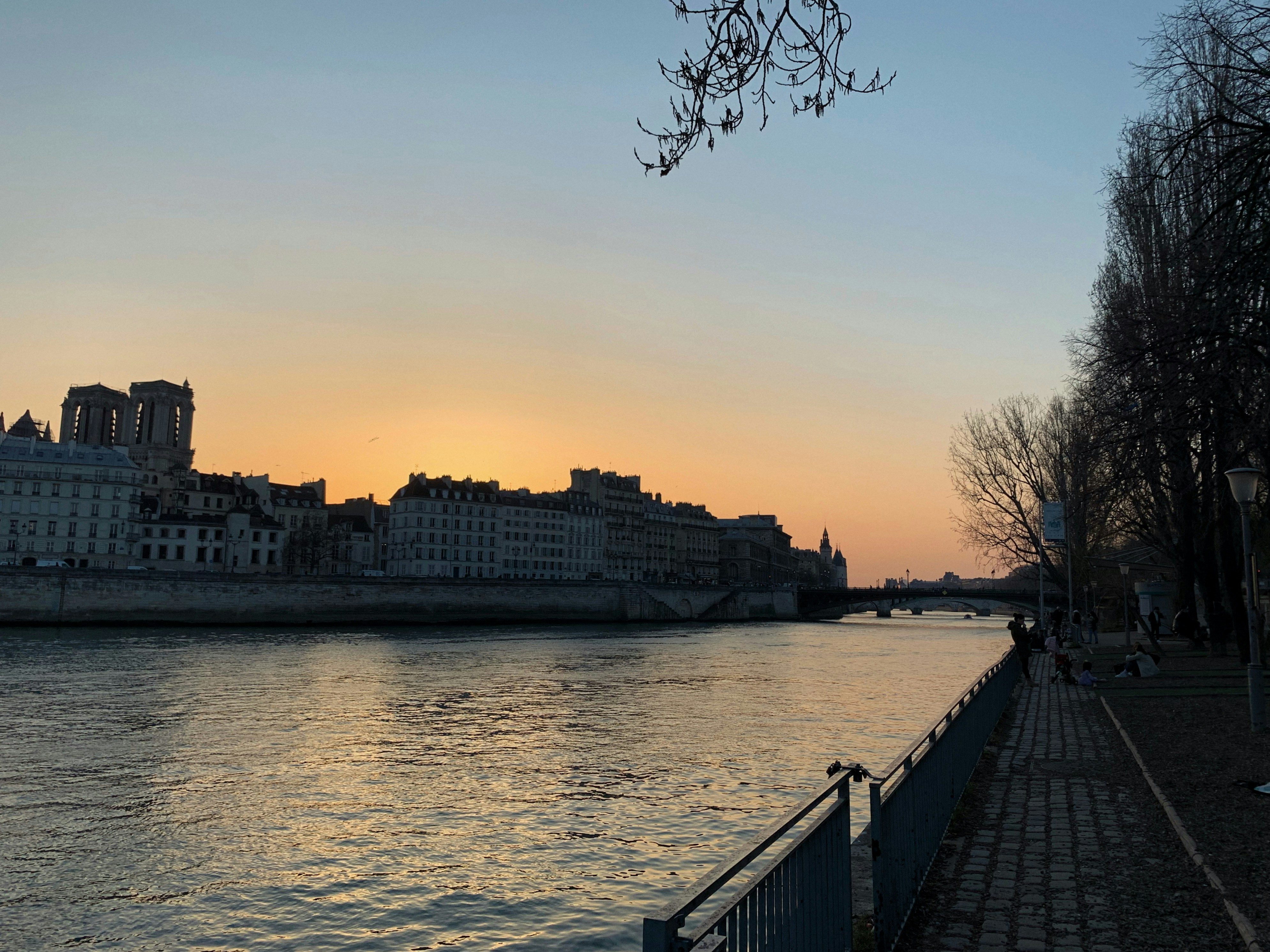 Serene view of the Seine River at dusk, with historic buildings lining the bank and a gentle glow on the water's surface.