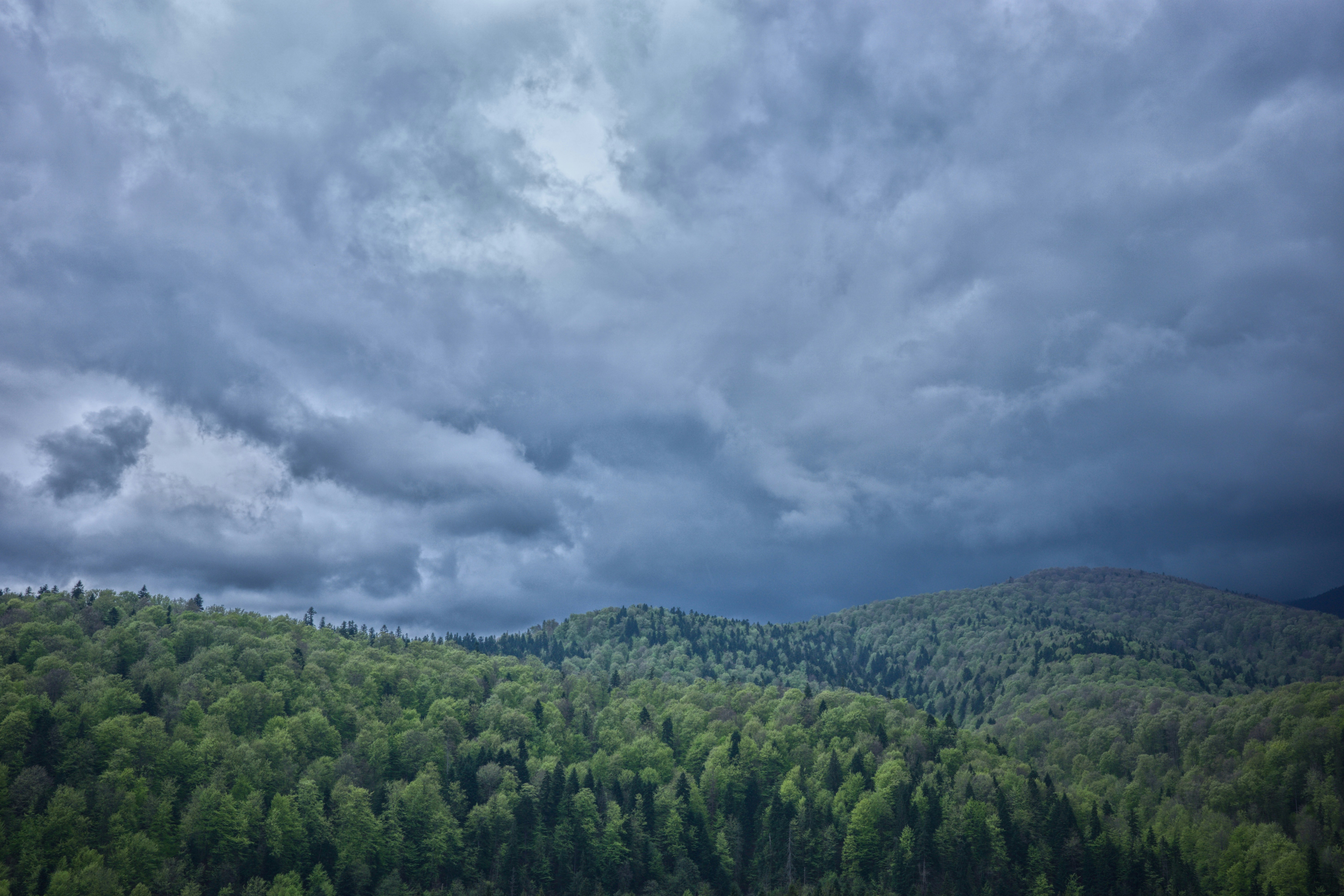 Lush green hills under a dramatic sky filled with dark, swirling clouds, hinting at an impending storm.