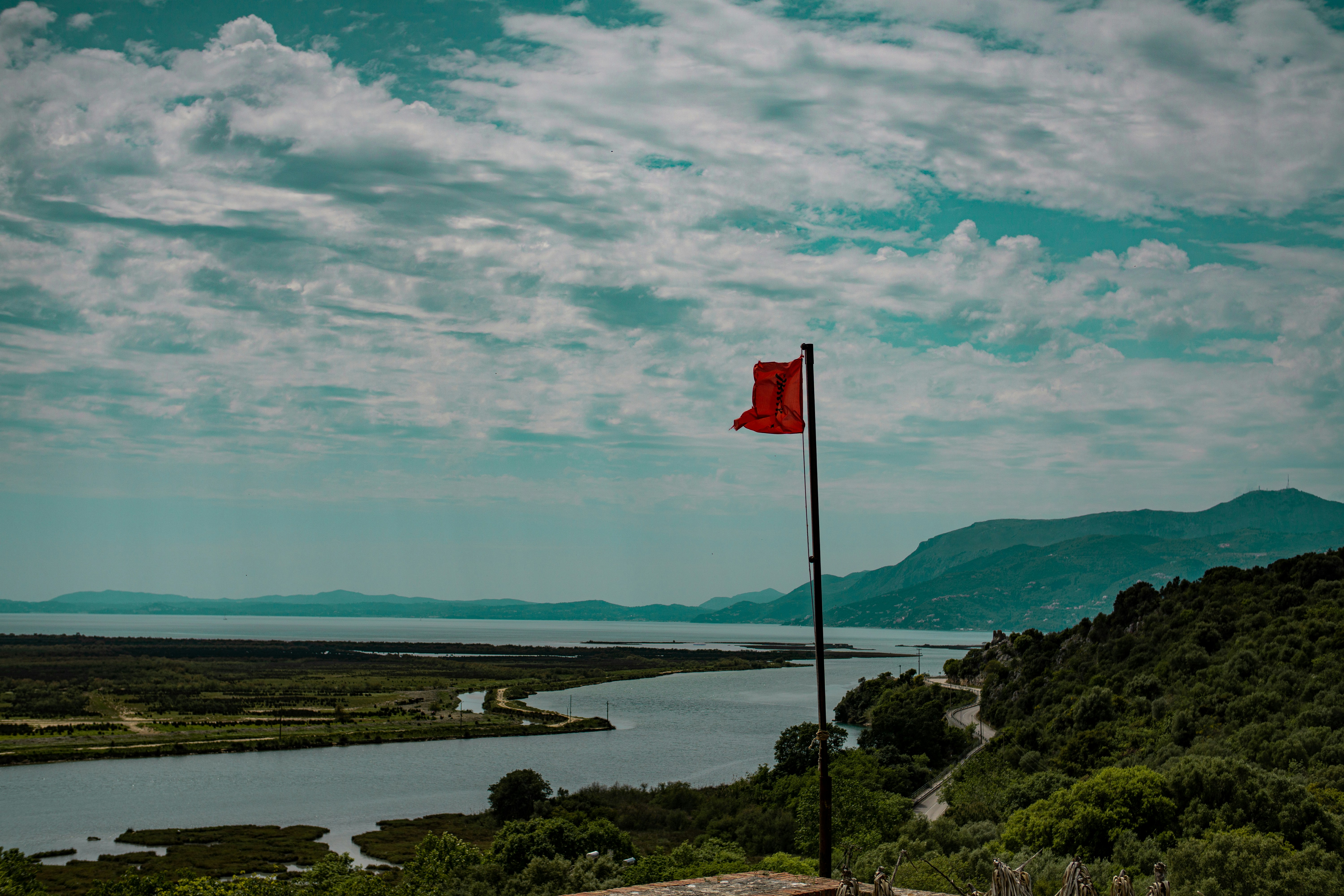 A vibrant red flag stands tall against a backdrop of serene waters and distant mountains, capturing the essence of tranquility in nature.