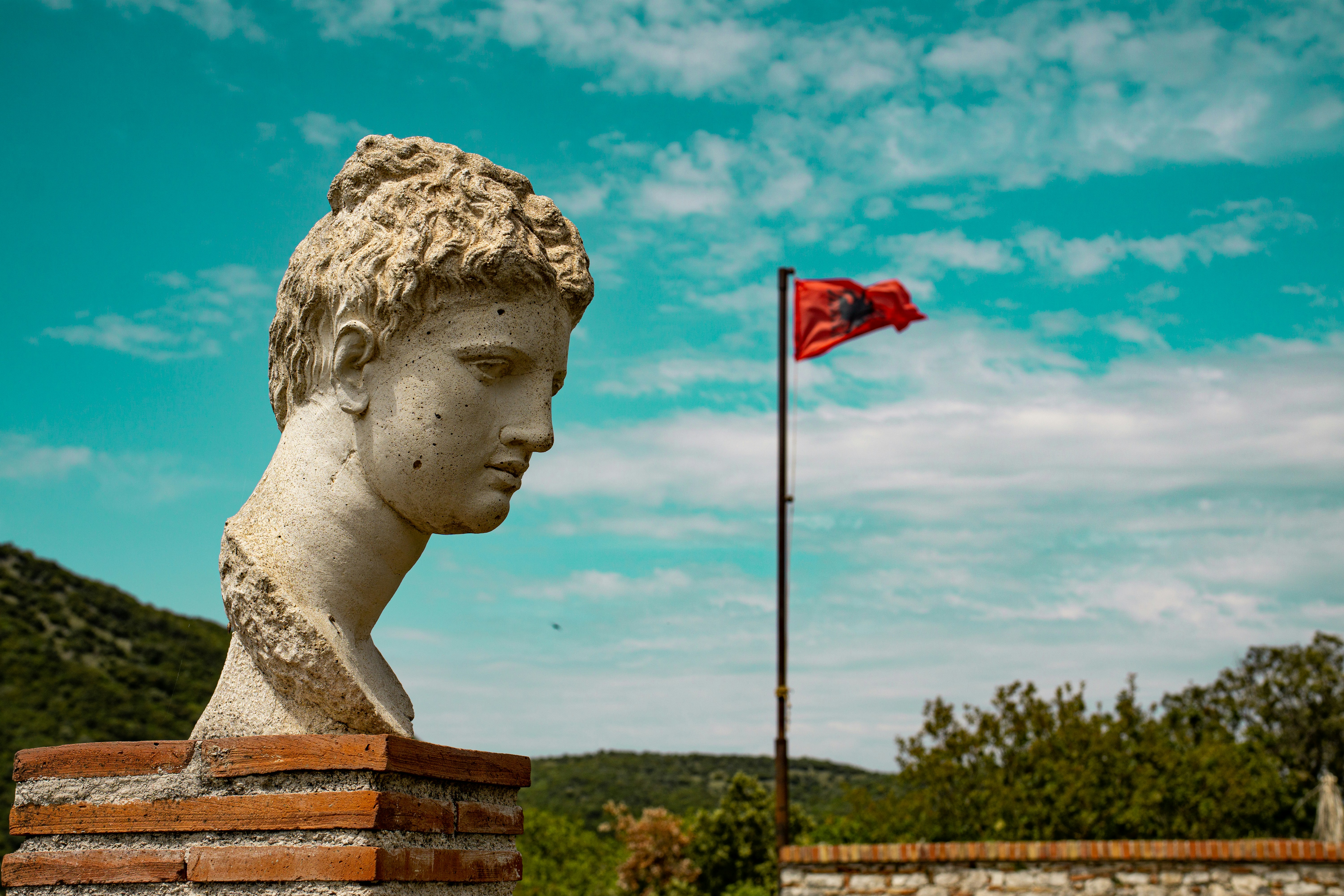 Contemplative Bust Under a Turquoise Sky and a Guarding Red Flag