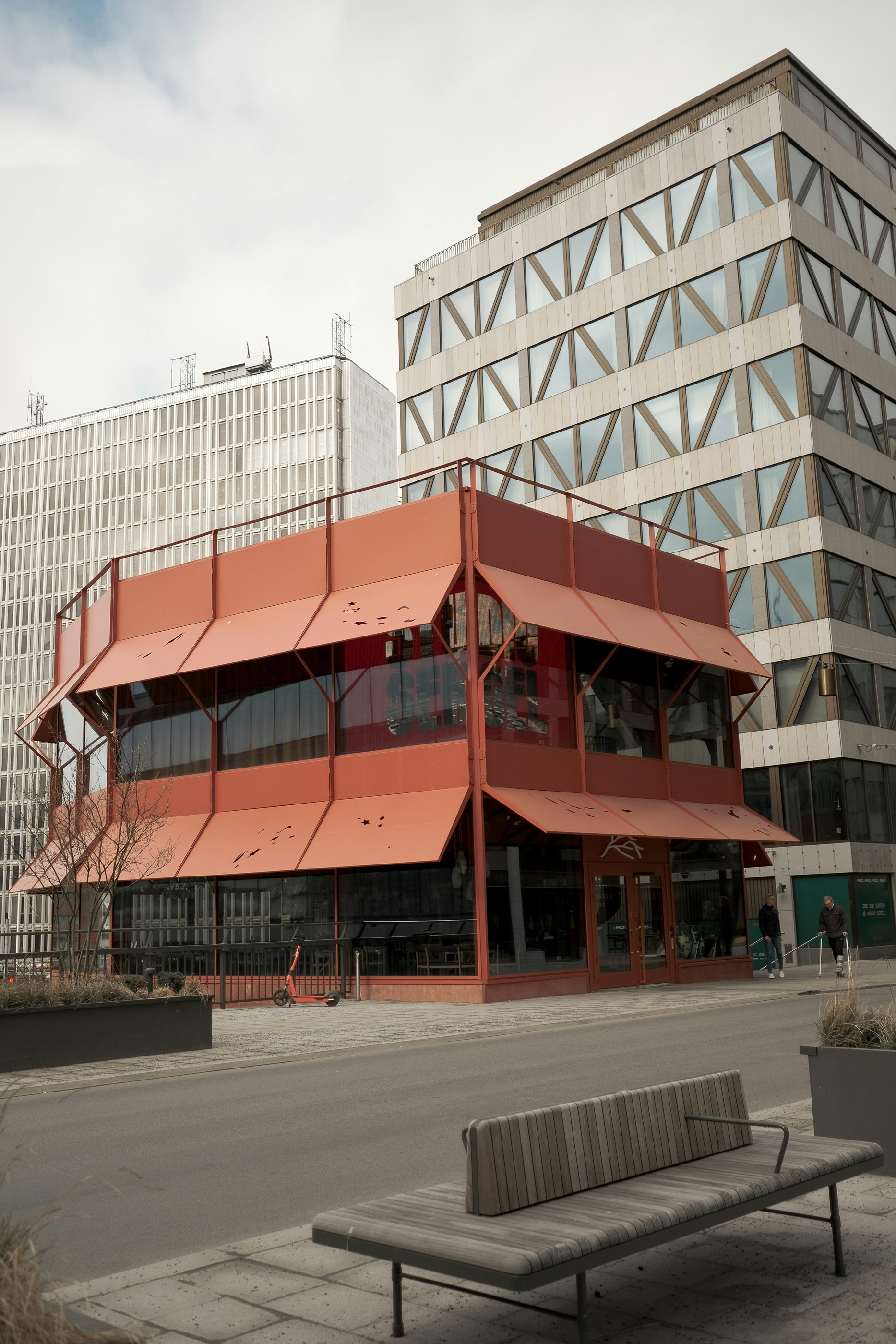 Angled Orange Pavilion Anchoring a Glass-Front Cityscape