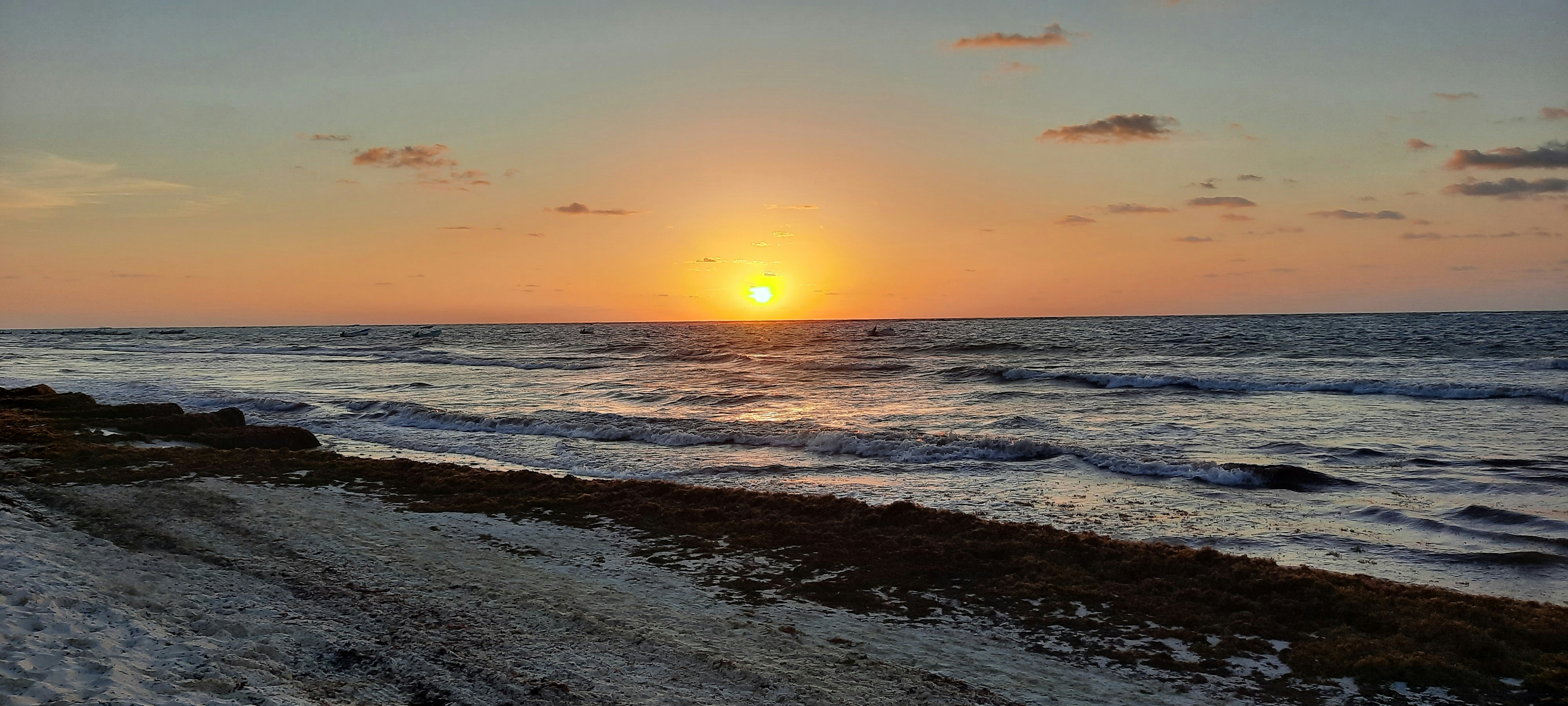 A beach with waves and the sun setting photo – Free Tulum Image on Unsplash
