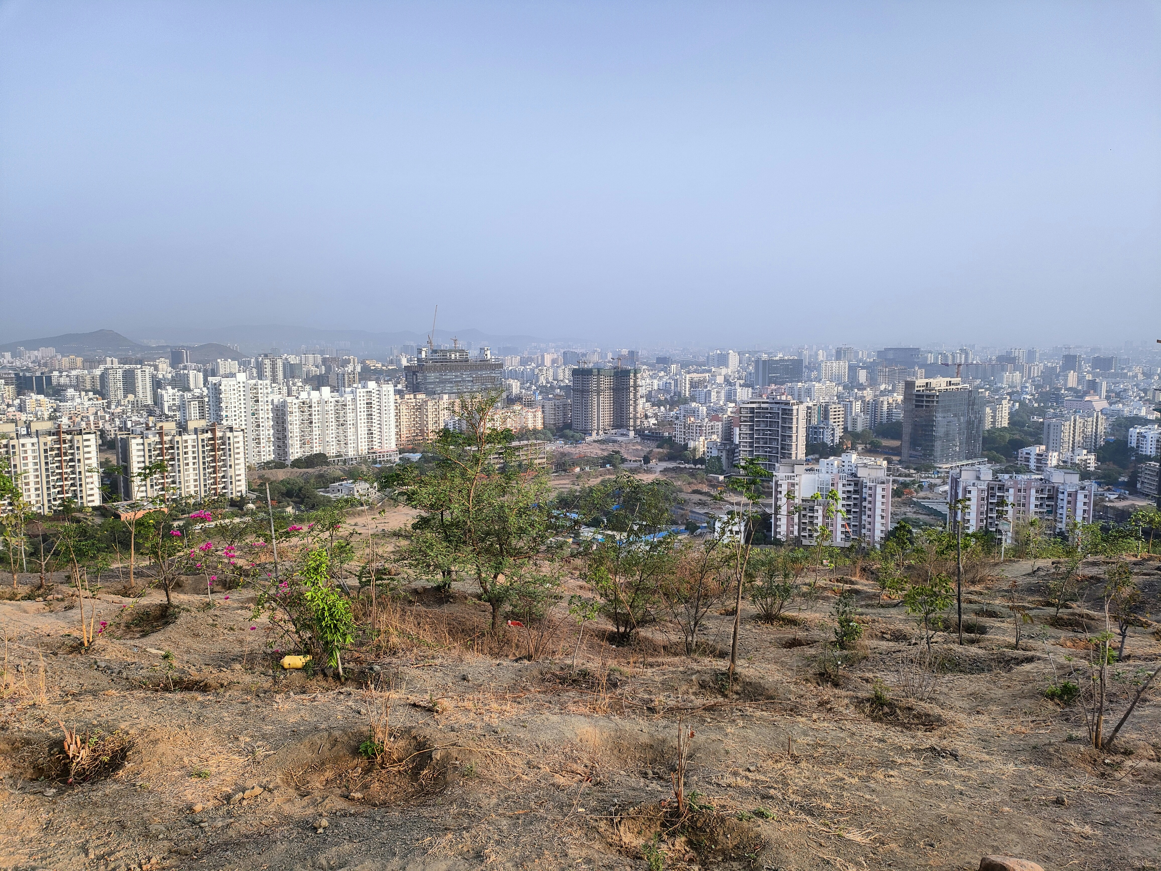 A panoramic view of a sprawling cityscape from a hillside, showcasing a mix of residential and commercial buildings under a clear sky.