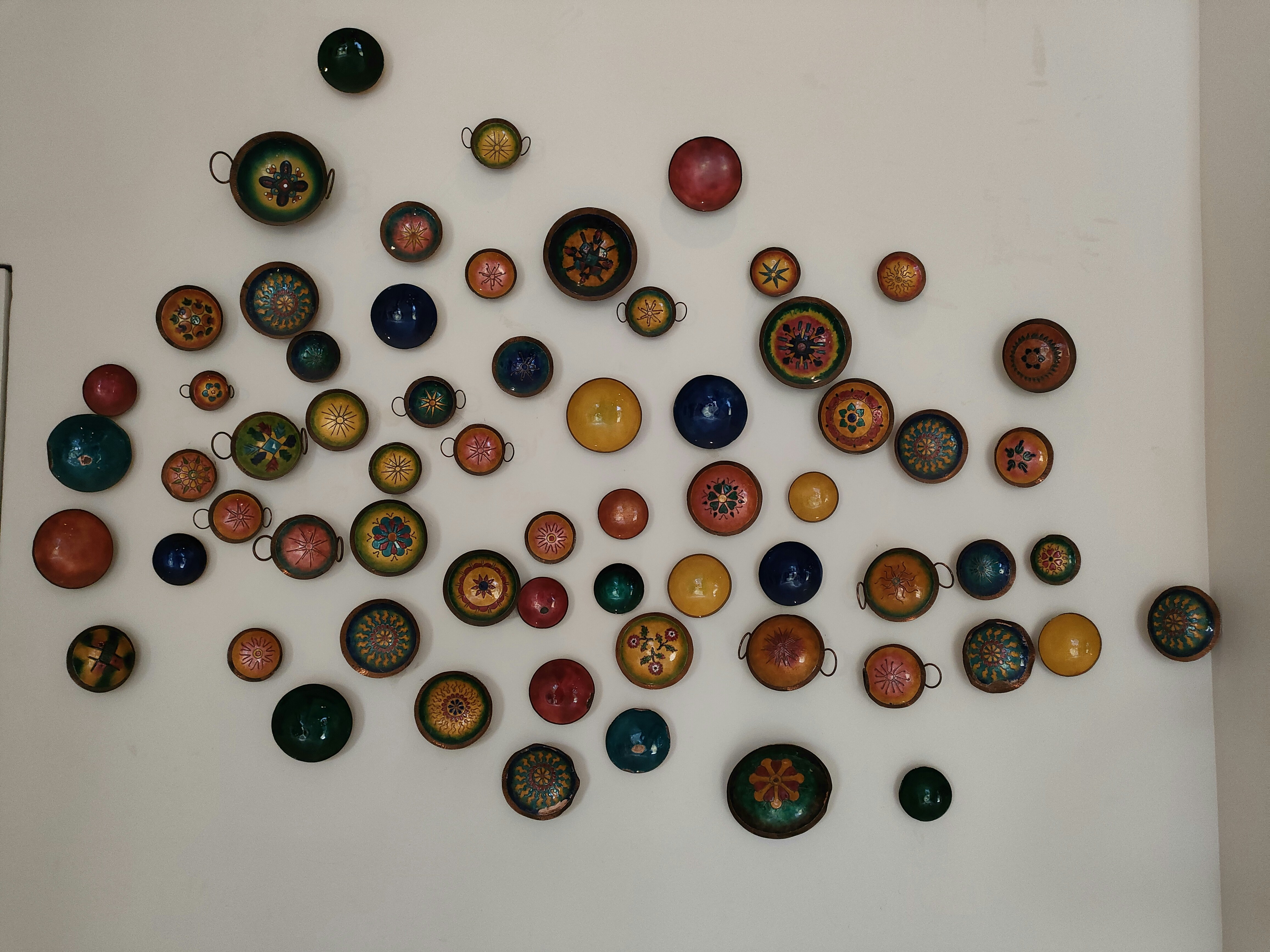 Vibrant collection of hand-painted circular decorative pieces arranged on a white wall, showcasing intricate designs and colors.