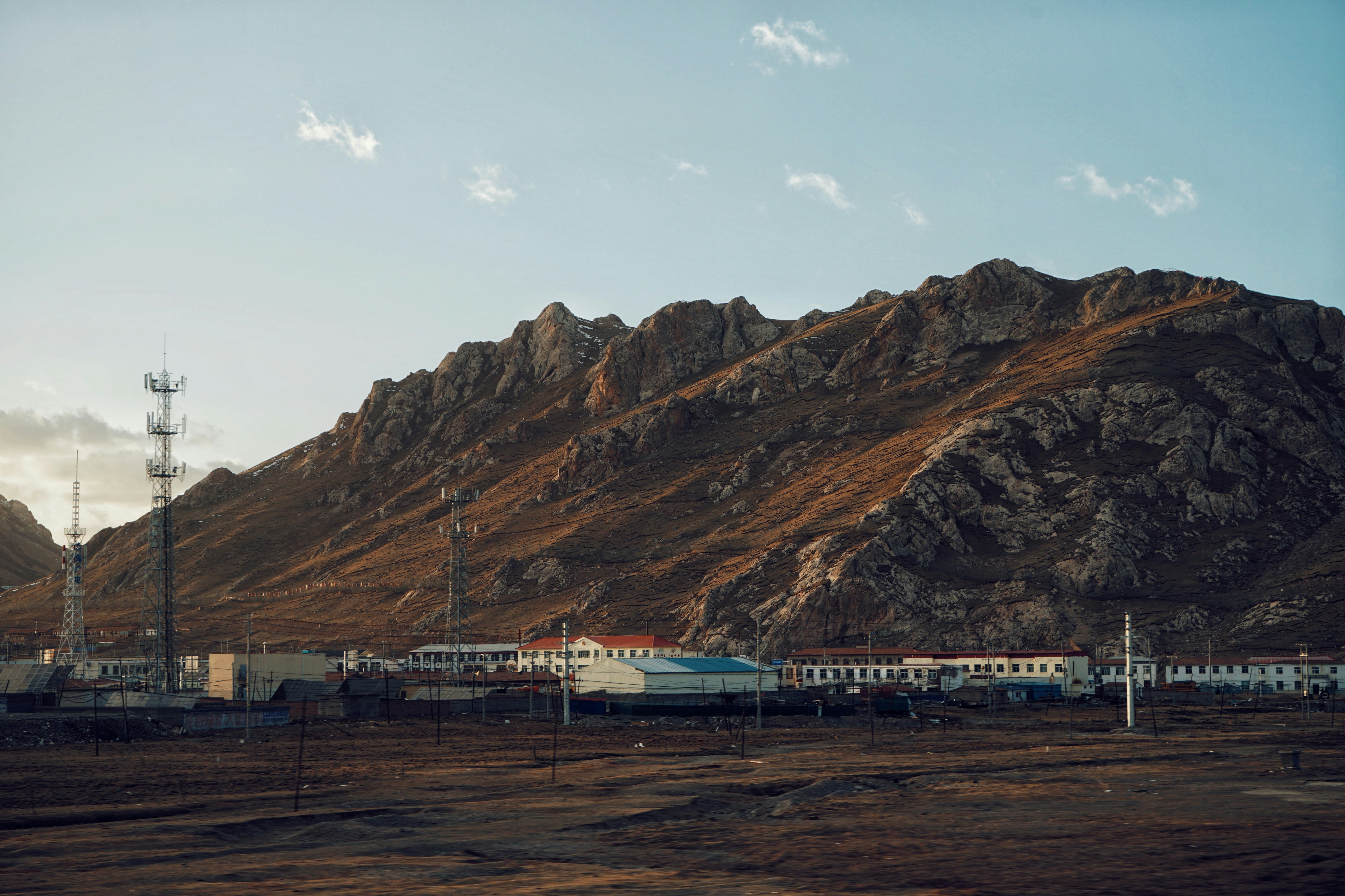 Telecommunication towers and buildings nestled at the base of rugged mountains under a clear sky.