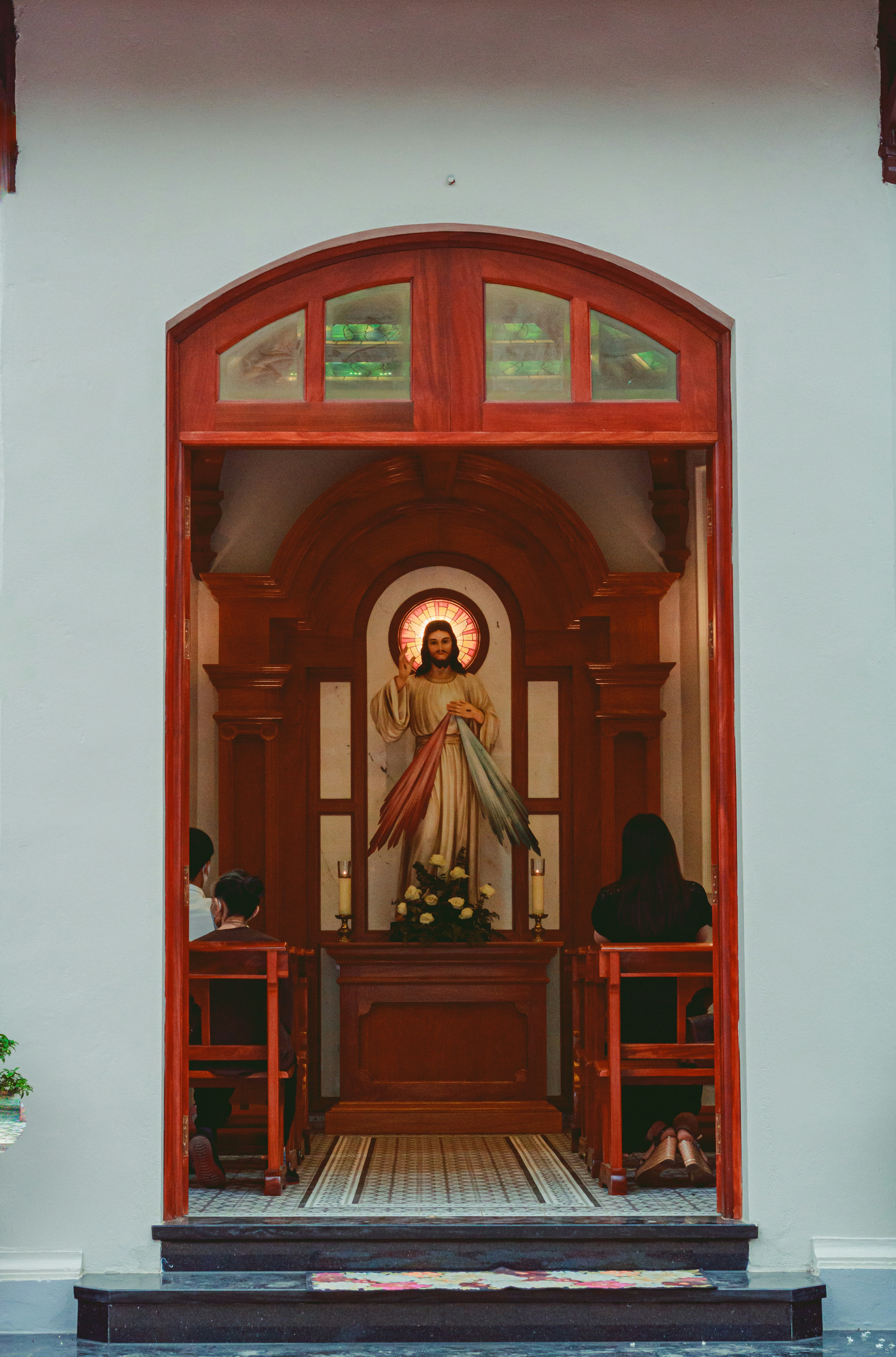 A serene chapel featuring a statue of Jesus with outstretched arms, surrounded by worshippers in quiet contemplation.