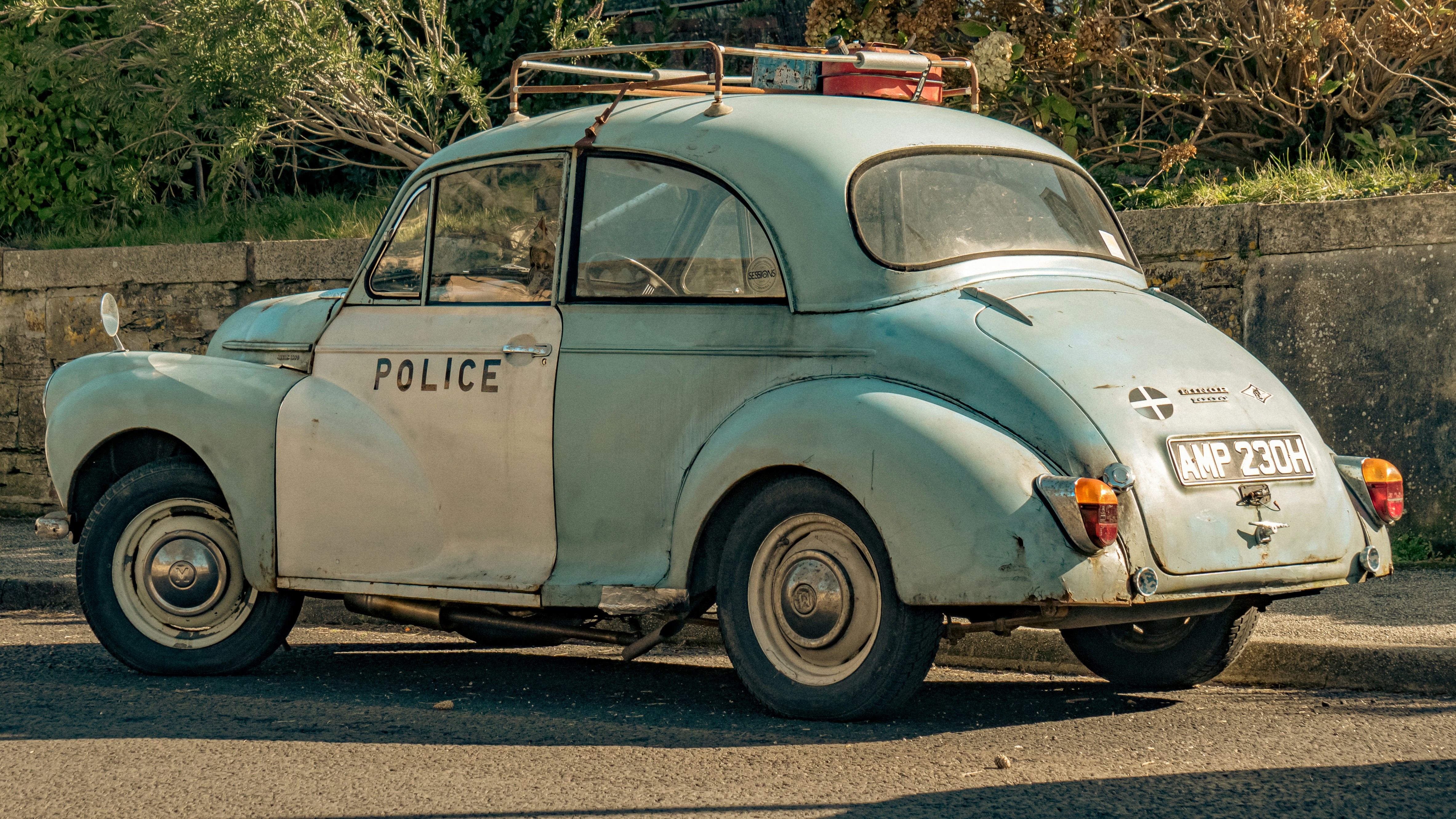 Classic police car from the mid-20th century parked on a quiet street, showcasing its retro design and faded paintwork.