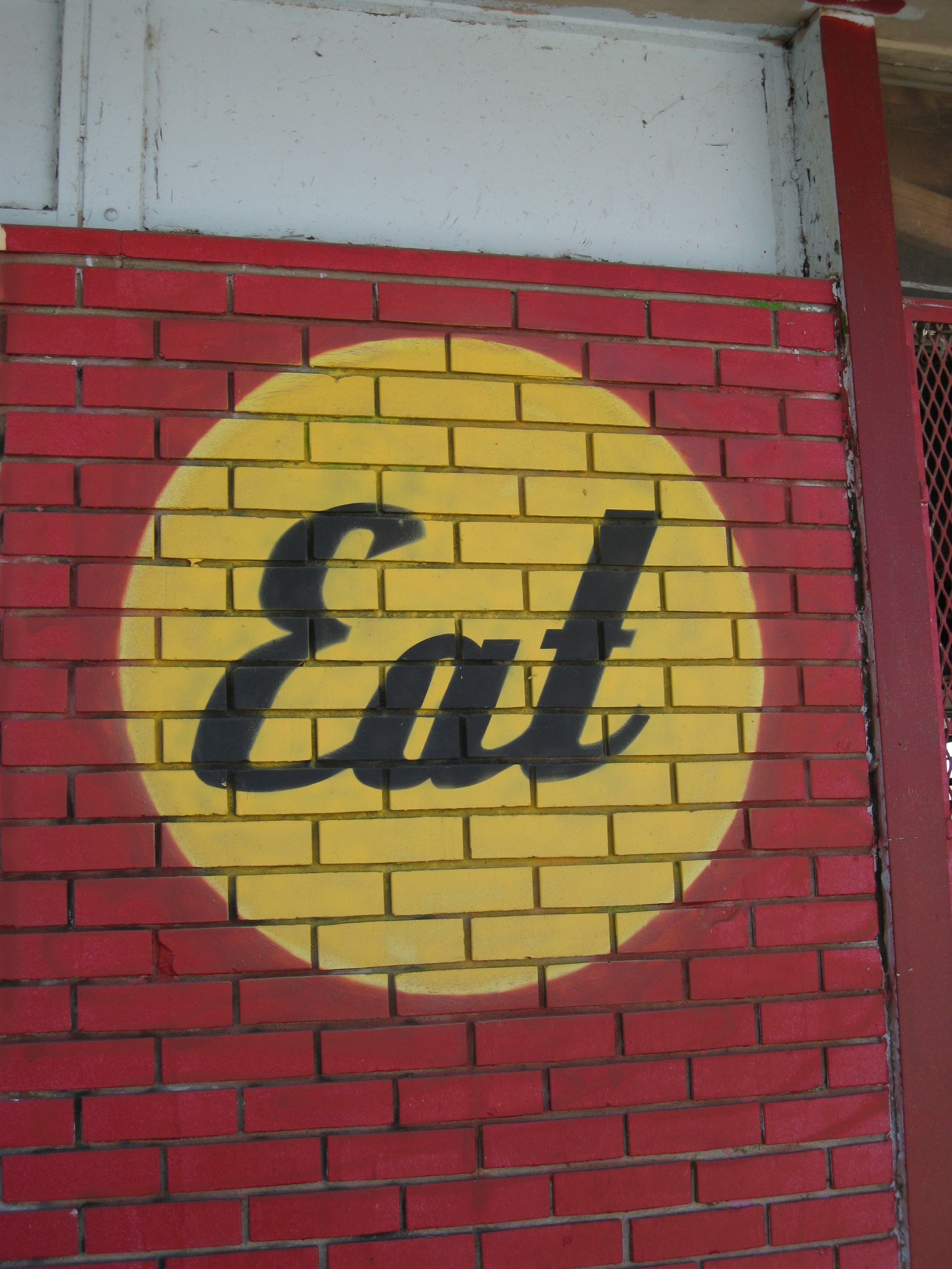 Painted mural of the word 'Eat' inside a yellow circle on a red brick wall.