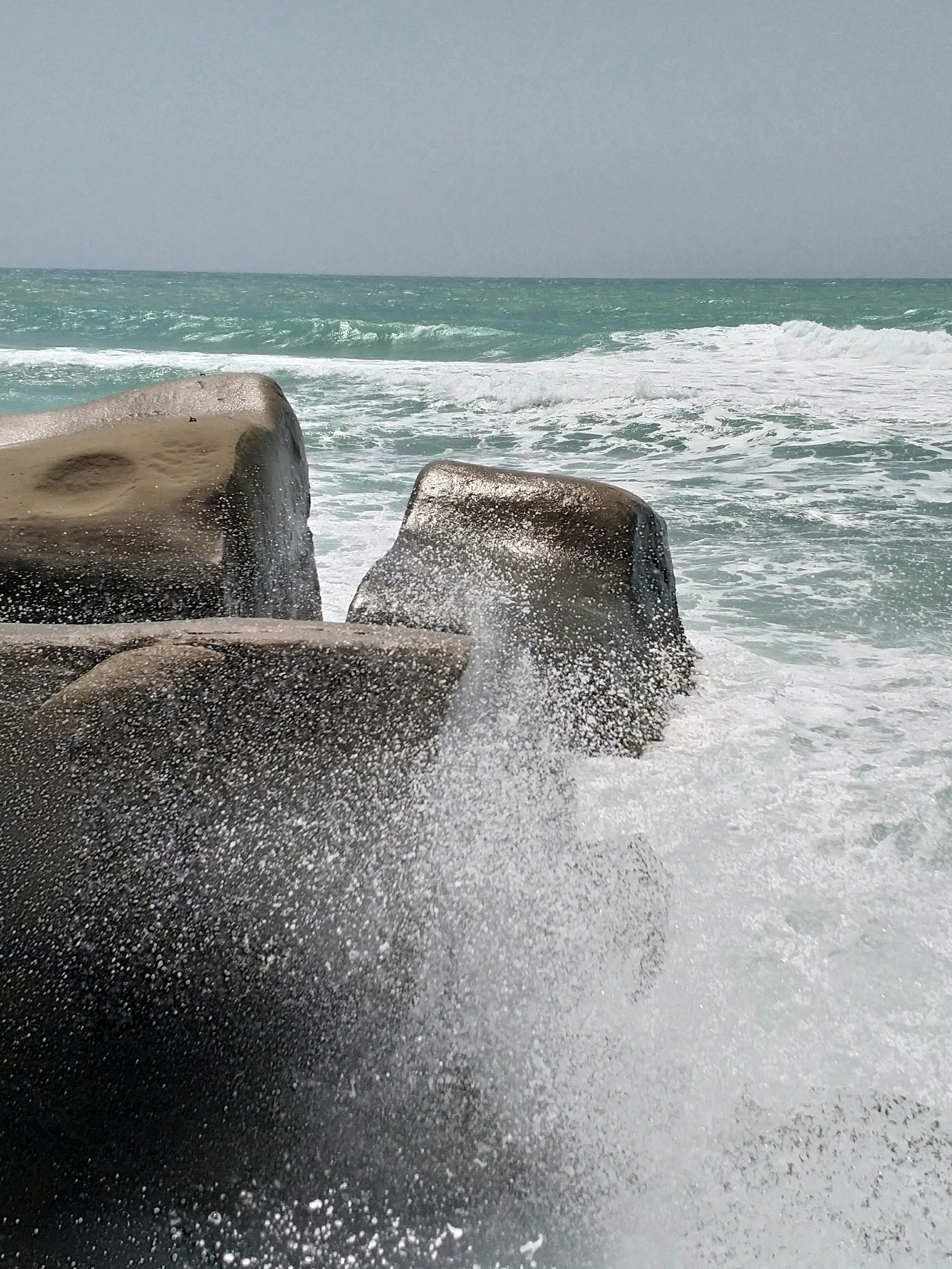 A concrete breakwater takes the brunt as turquoise waves collide, spraying mist over weathered rocks.