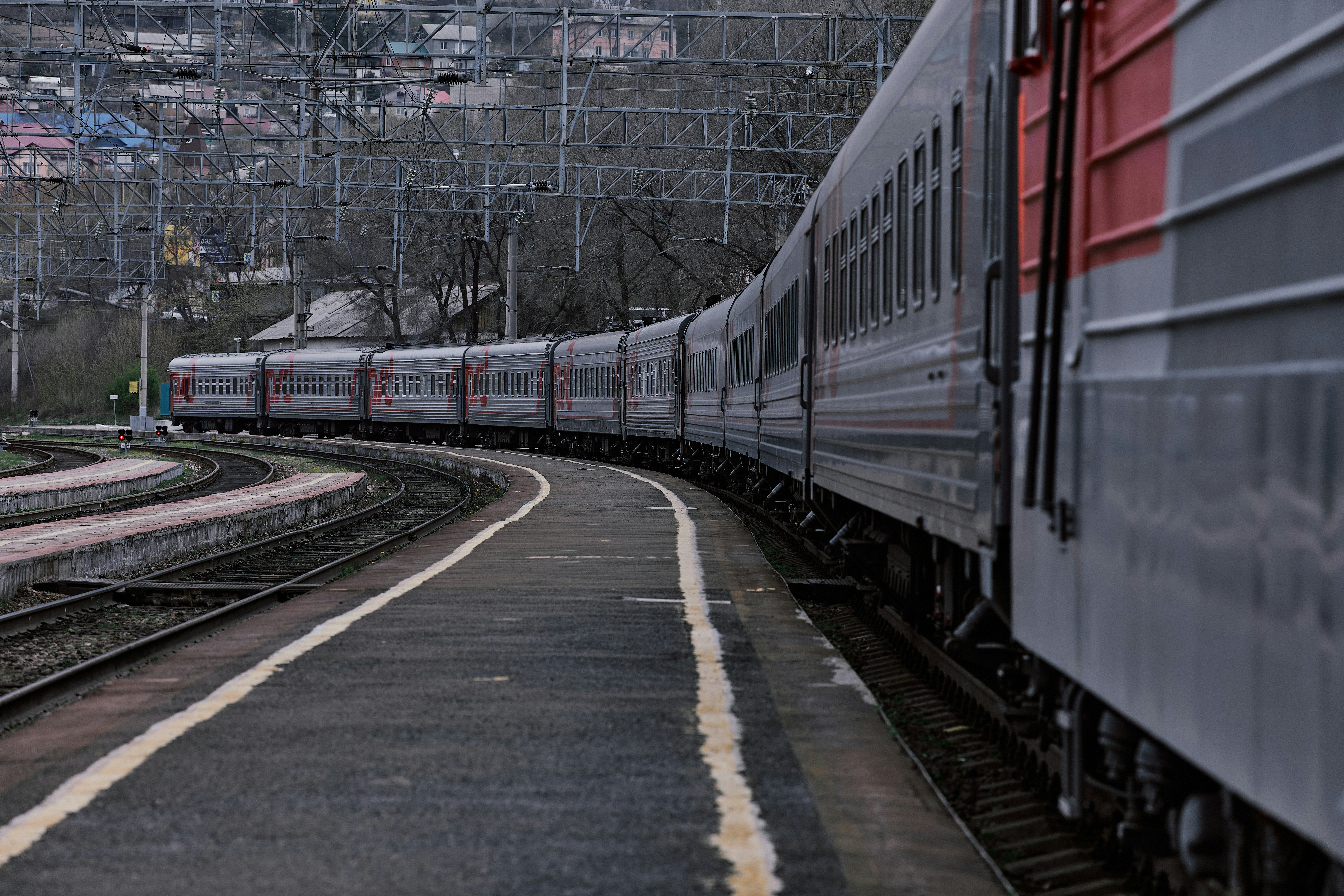 Long train curving through a misty landscape with overhead power lines and distant hills.