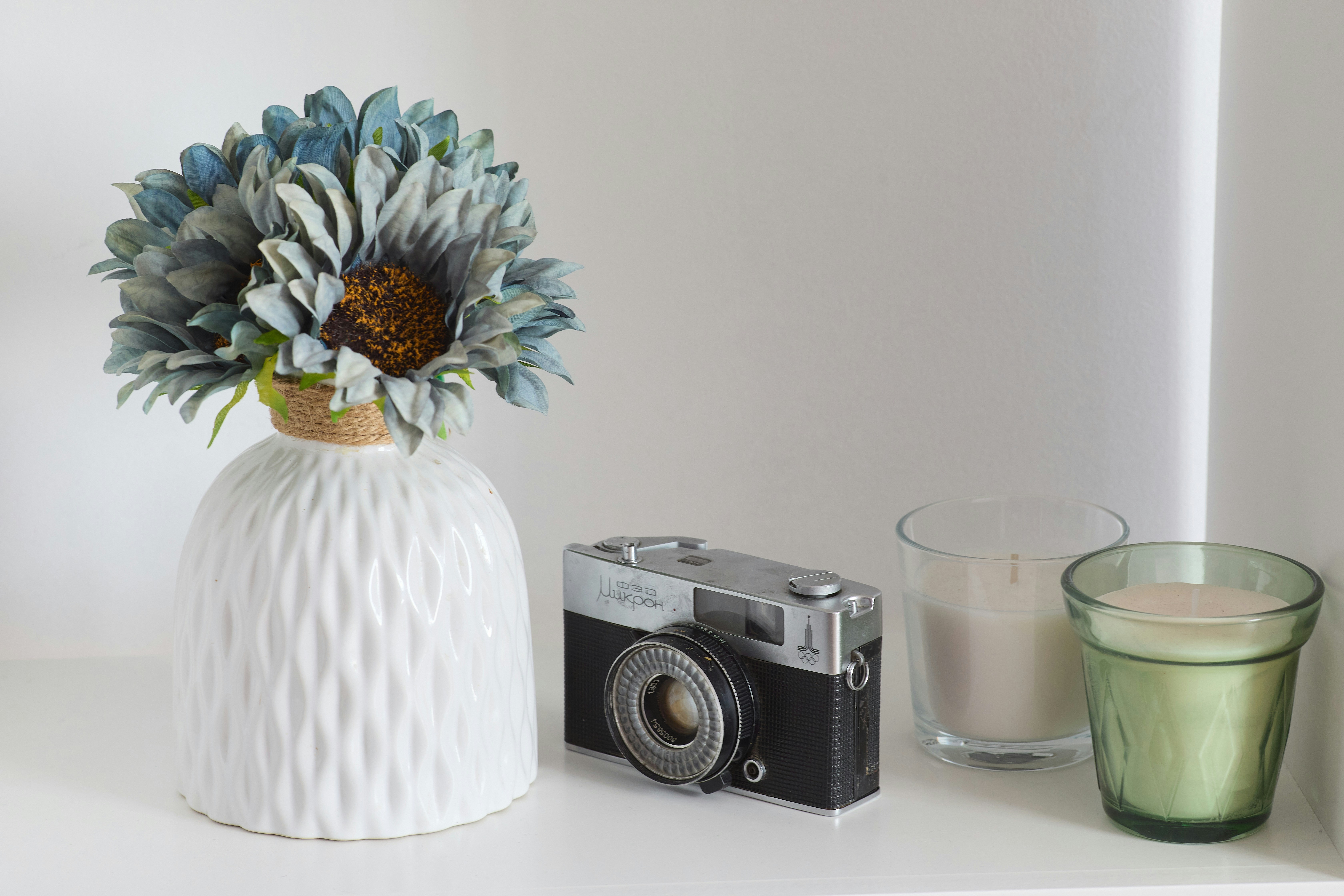 Vintage camera beside a vase with blue flowers and two candles on a white surface.
