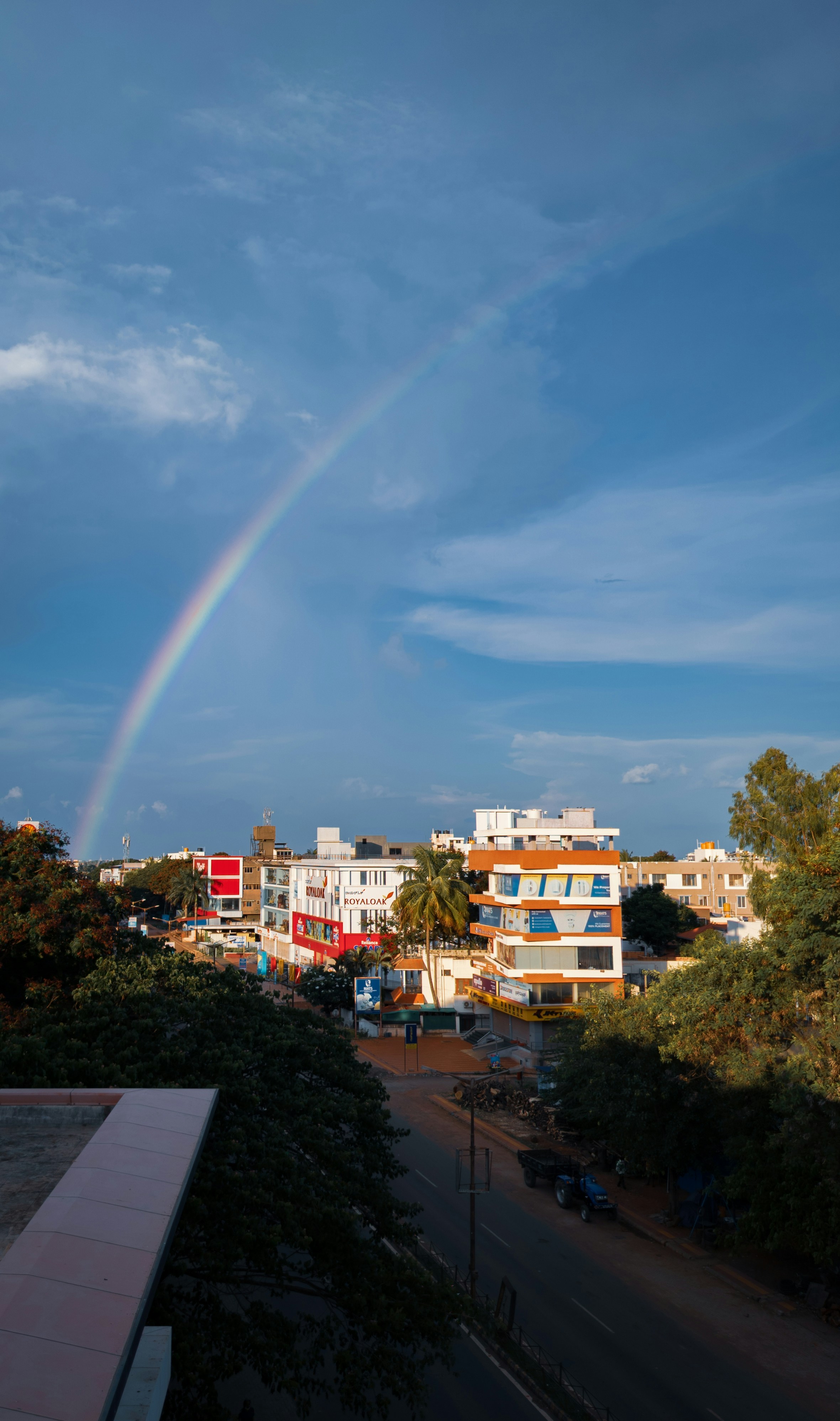 A vibrant urban scene featuring colorful buildings and lush trees, with a rainbow arching across a clear blue sky.