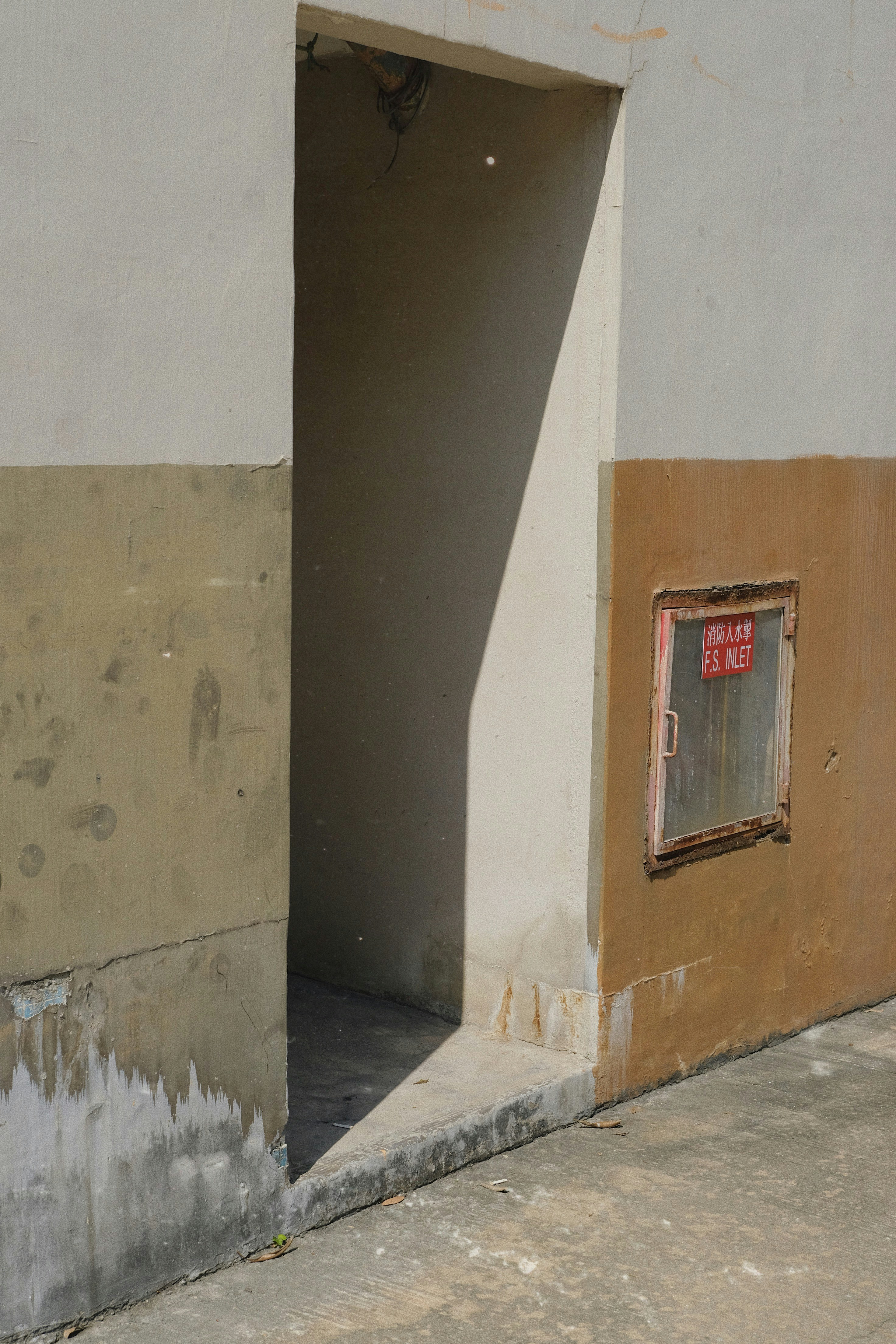 An empty doorway framed by textured walls, with a small window displaying a faded sign. The interplay of light and shadow creates a sense of mystery.