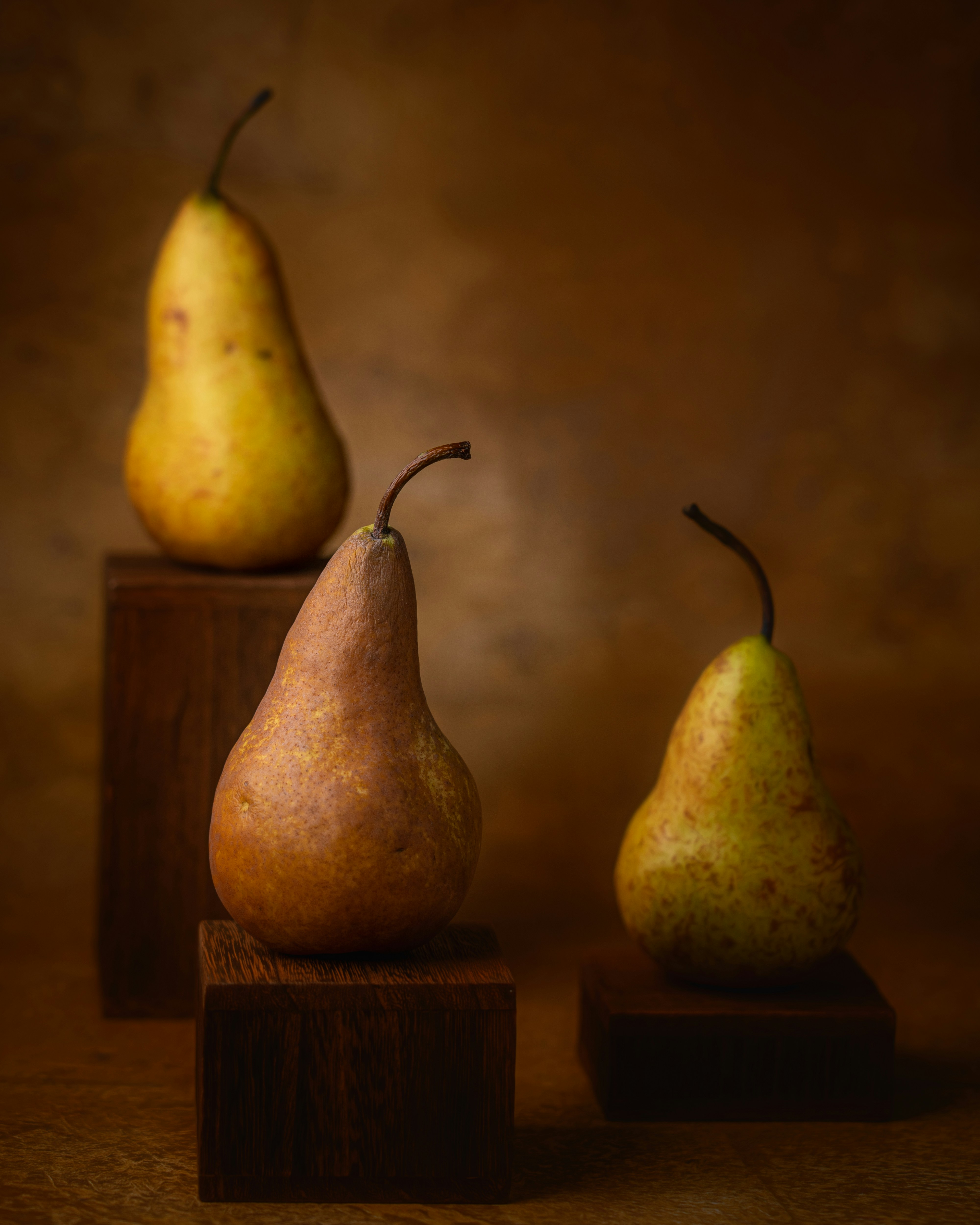 Three pears of varying hues and shapes elegantly arranged on wooden blocks against a warm, textured background.