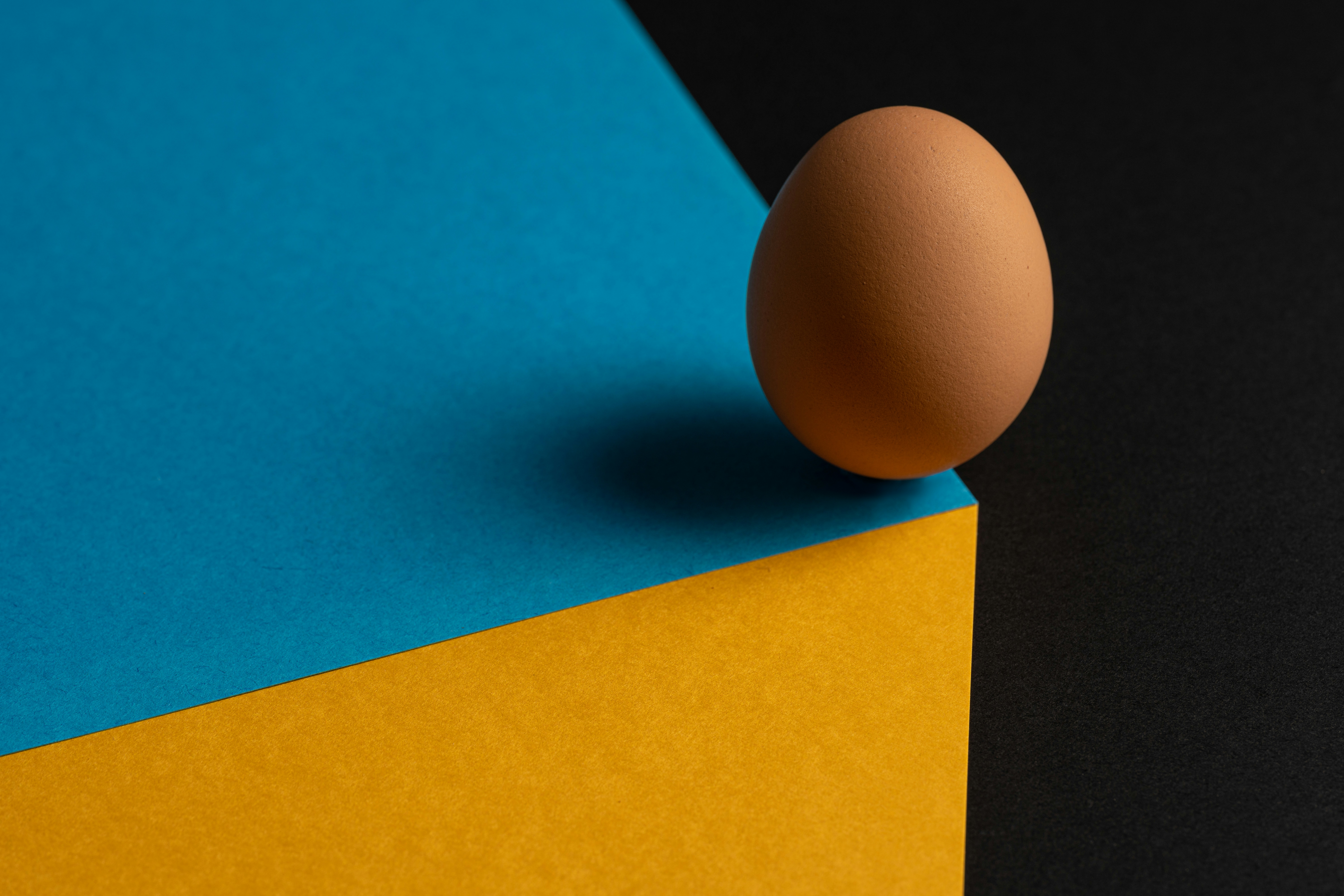 Brown egg poised delicately on the edge of a vibrant blue and yellow geometric surface.