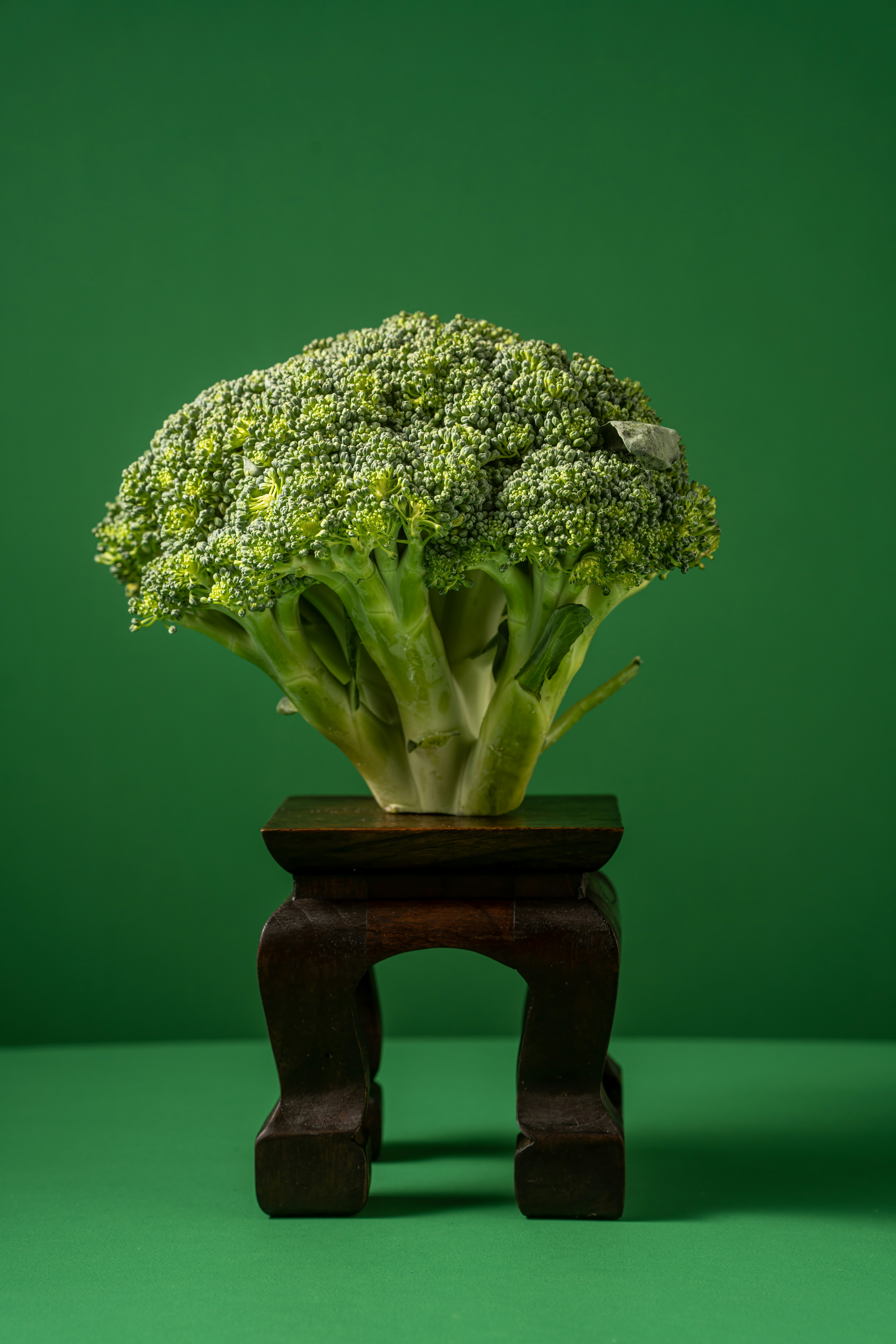 Broccoli displayed on a wooden pedestal against a vibrant green backdrop, showcasing its rich texture and color.