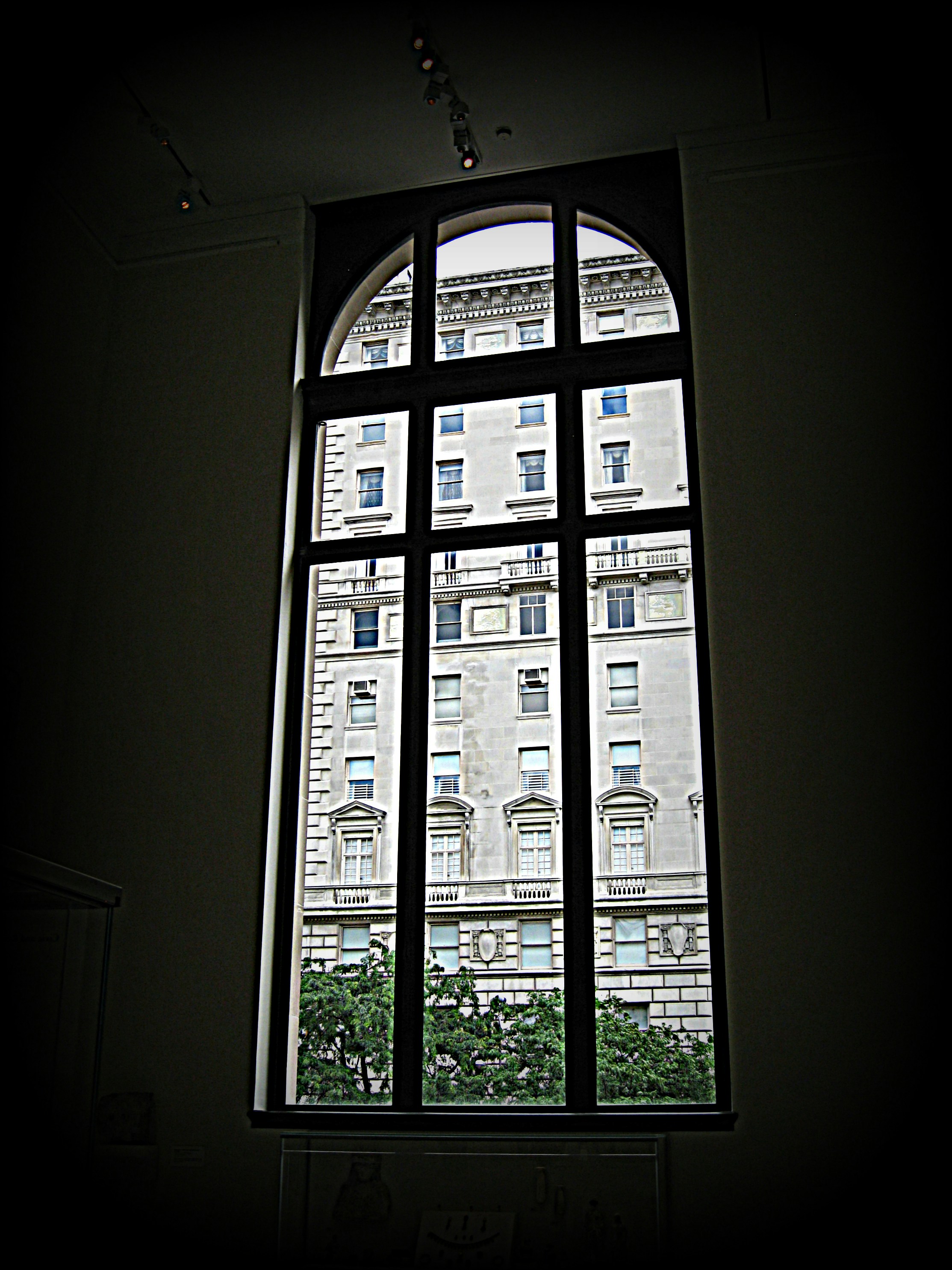 View of a historic building framed by a large, arched window, showcasing intricate architectural details and greenery below.