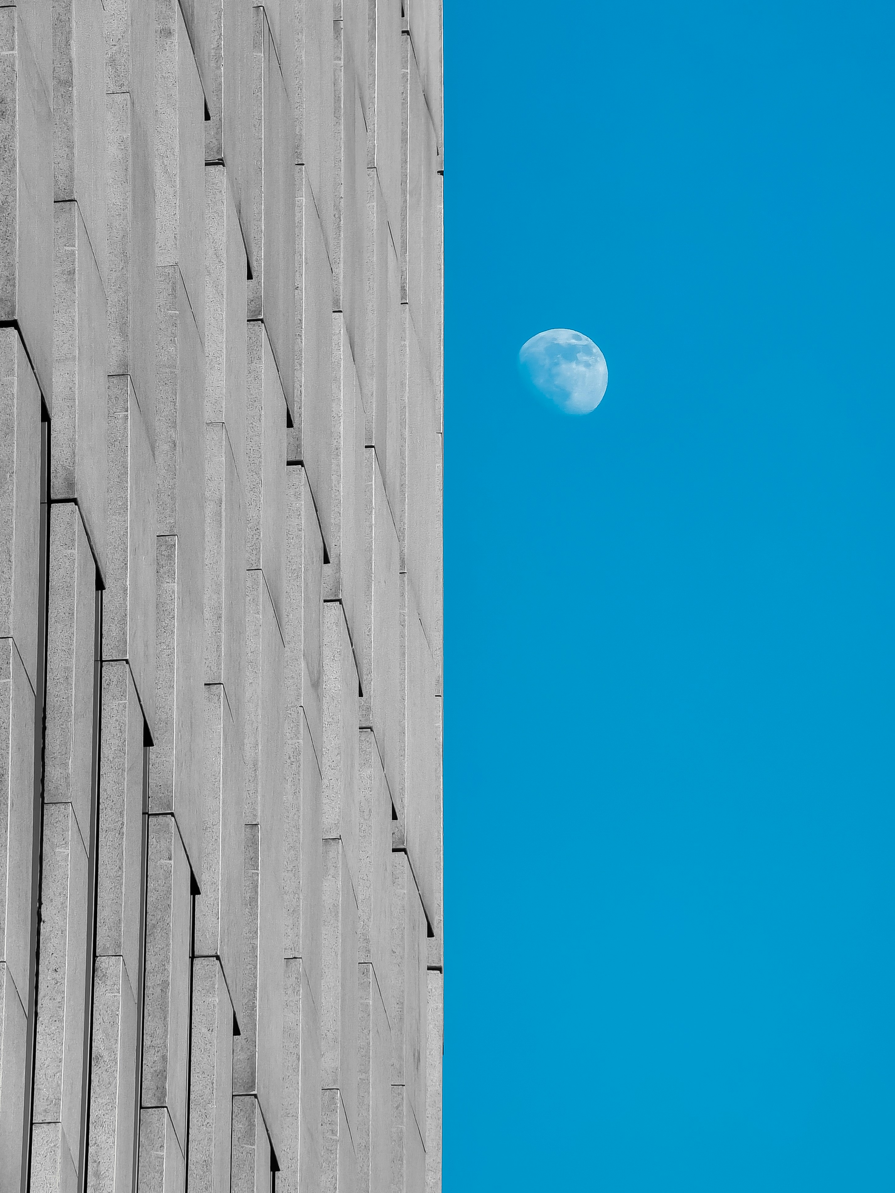 Monochrome textured concrete wall occupies the left with a bold blue sky and a small moon on the right, emphasizing contrast and minimalism.