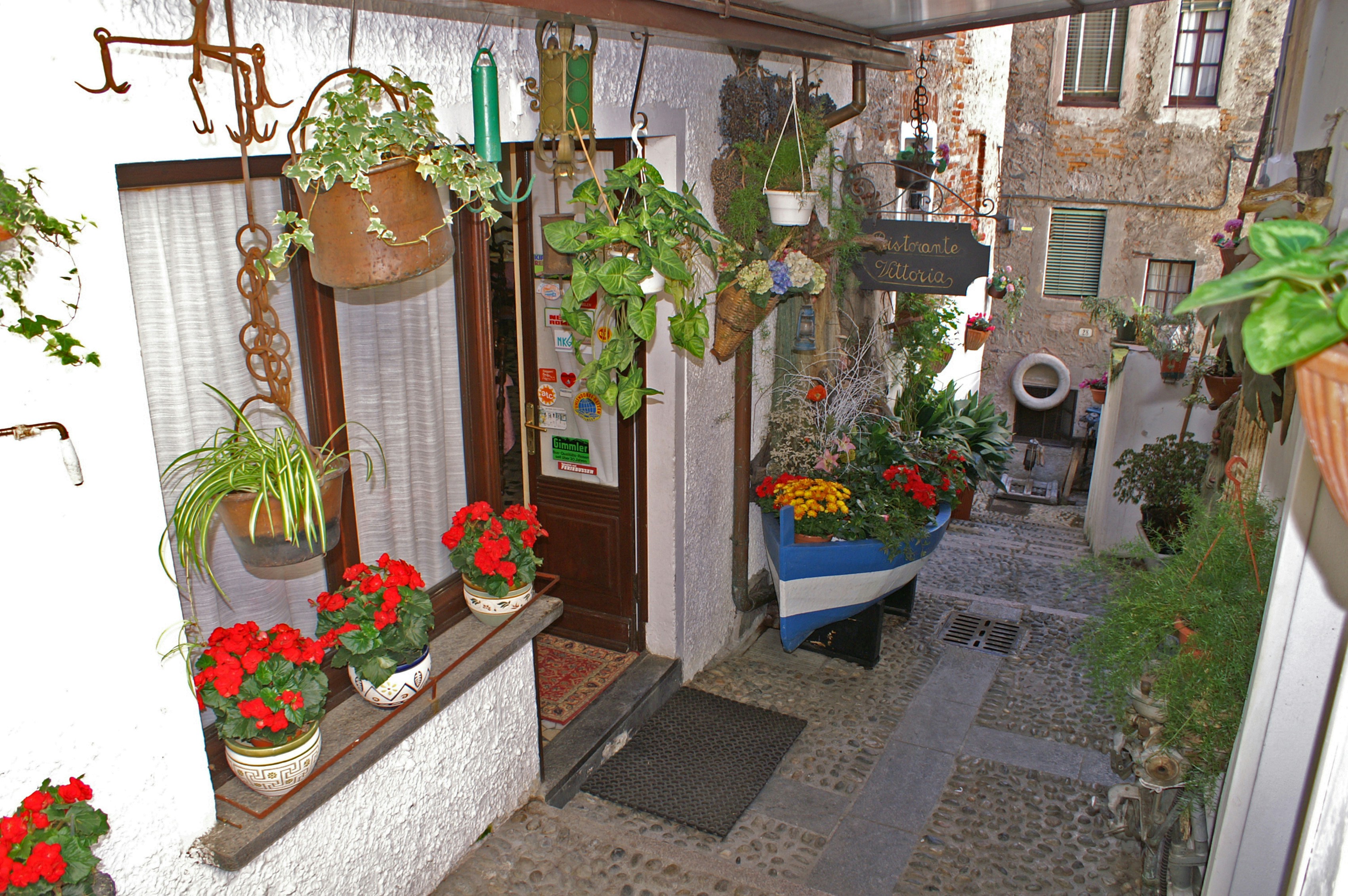 Quaint alley adorned with vibrant flowers and greenery, leading to a cozy entrance. A blend of rustic charm and lively colors draws the eye.