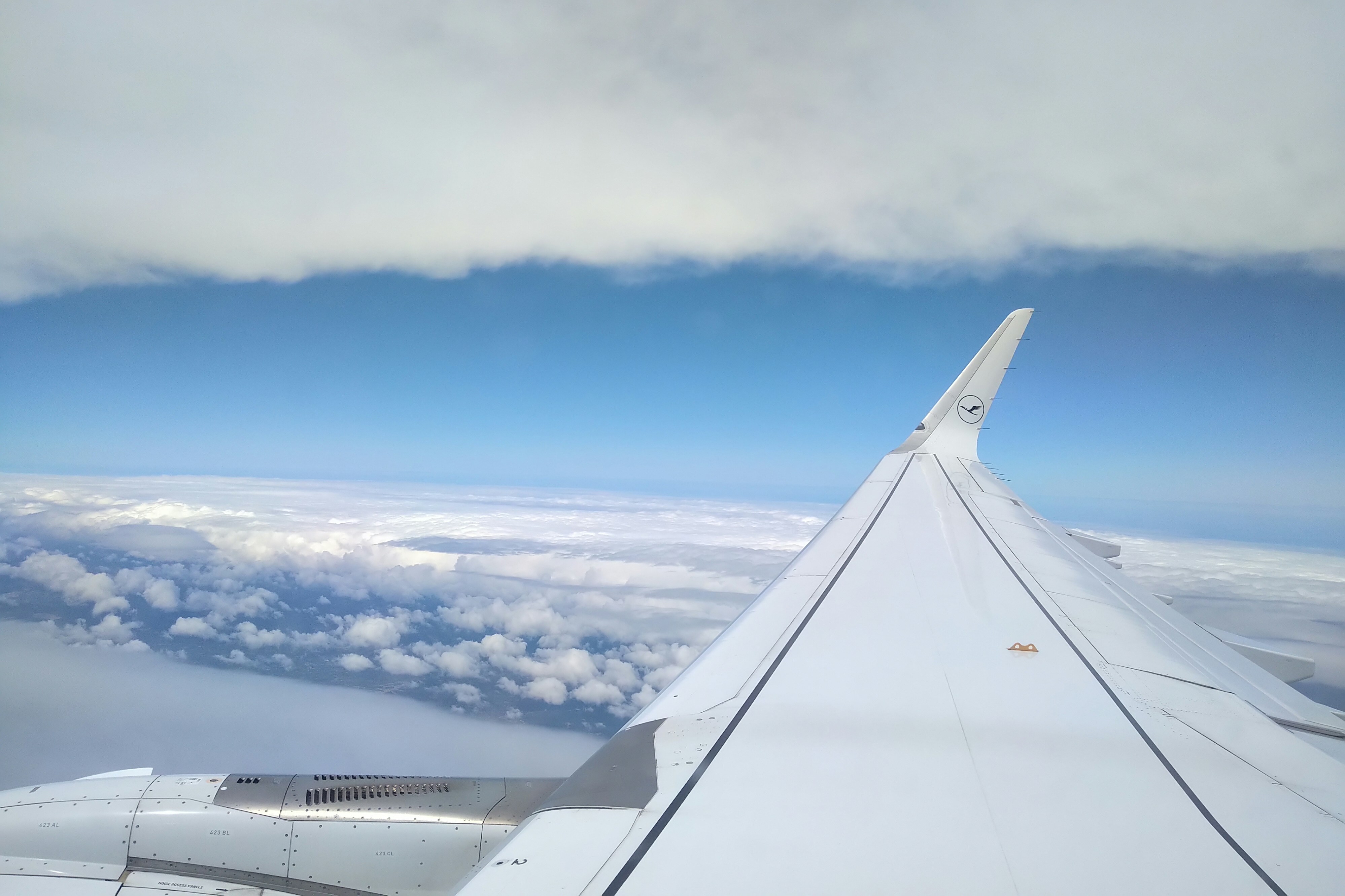 Airplane wing extending over a sea of clouds under a clear blue sky.