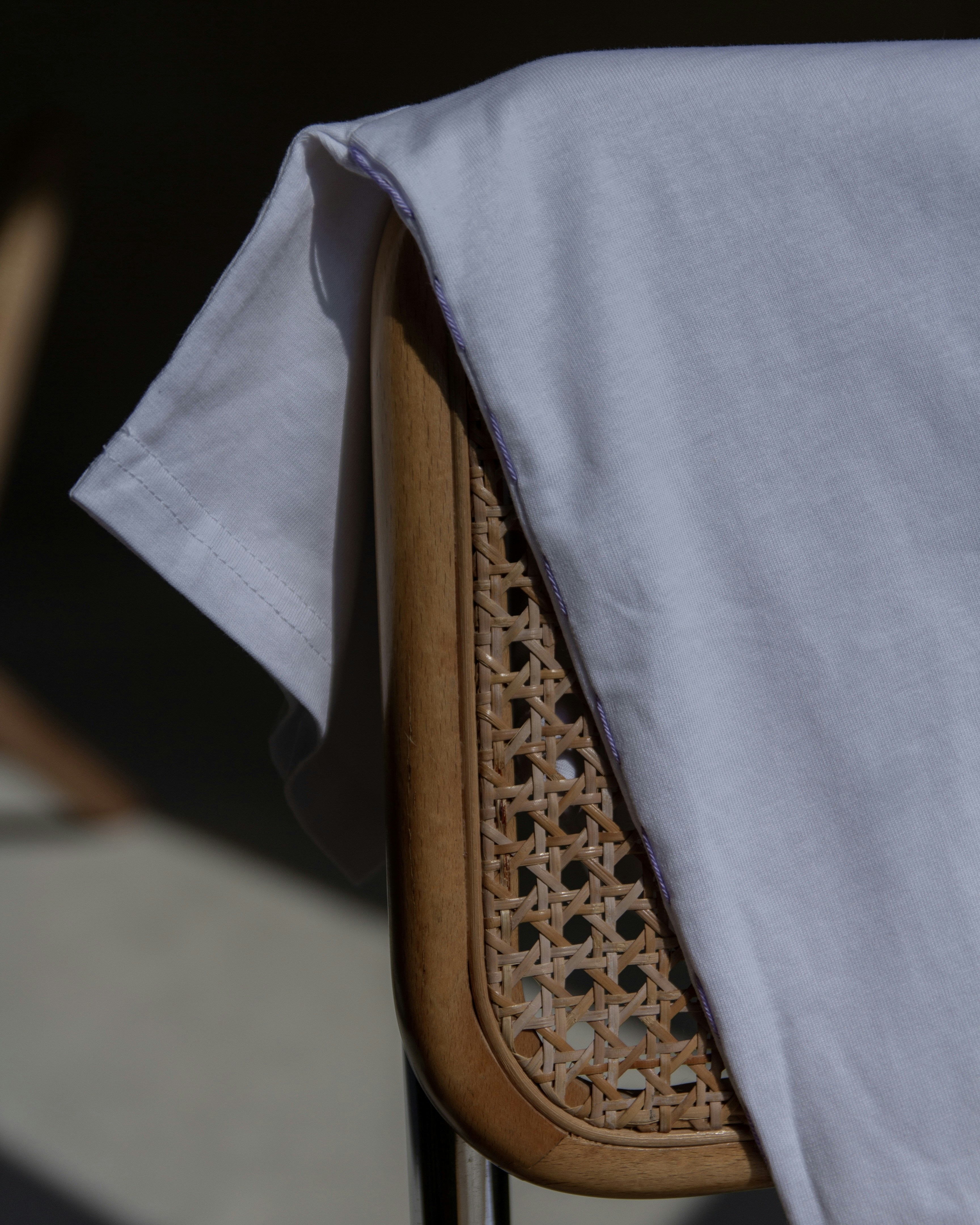 A white fabric drapes elegantly over a woven chair, highlighting the interplay of texture and light in a minimalist setting.