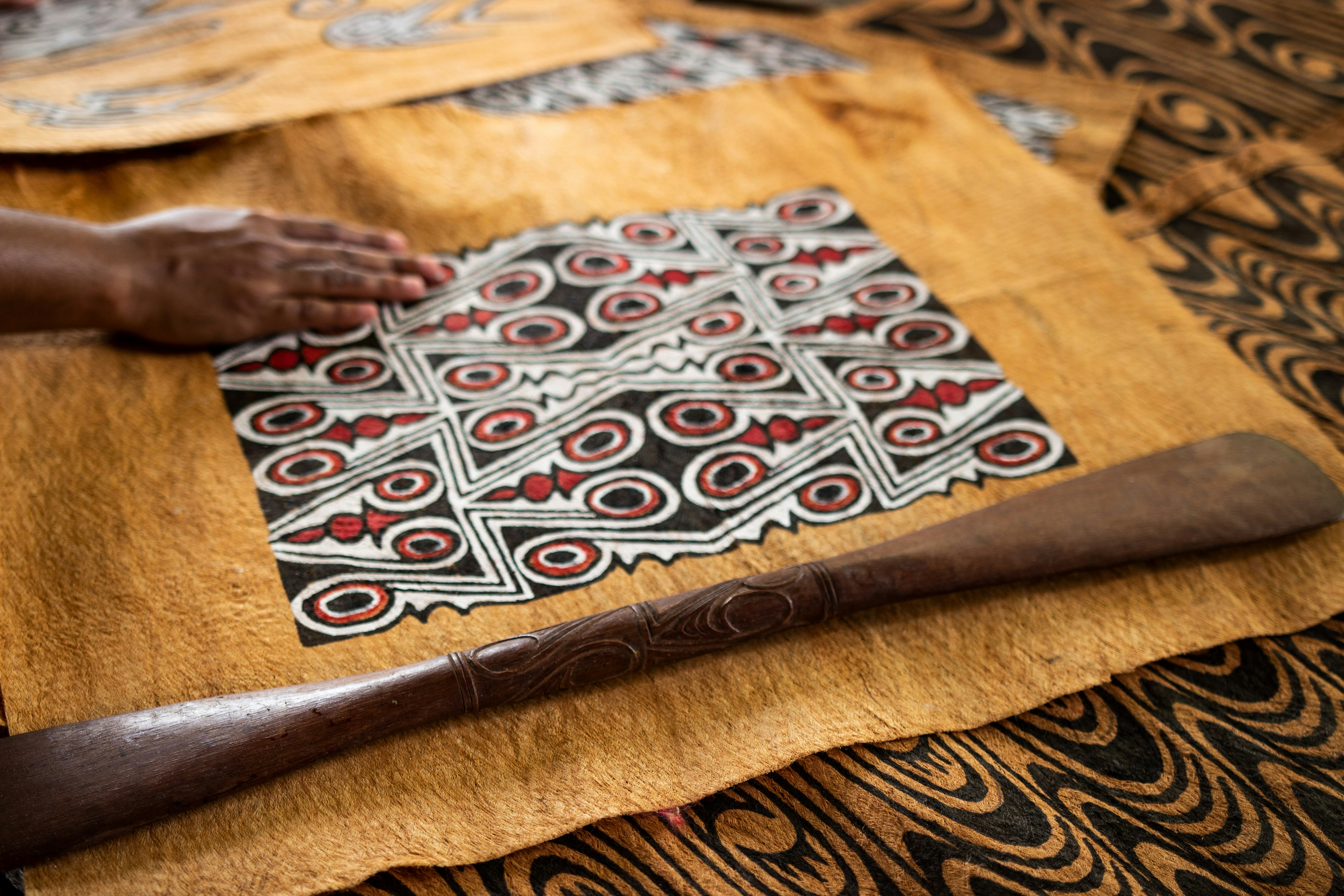 Geometric Tile Under a Hand on Golden Fabric with a Carved Wooden Baton