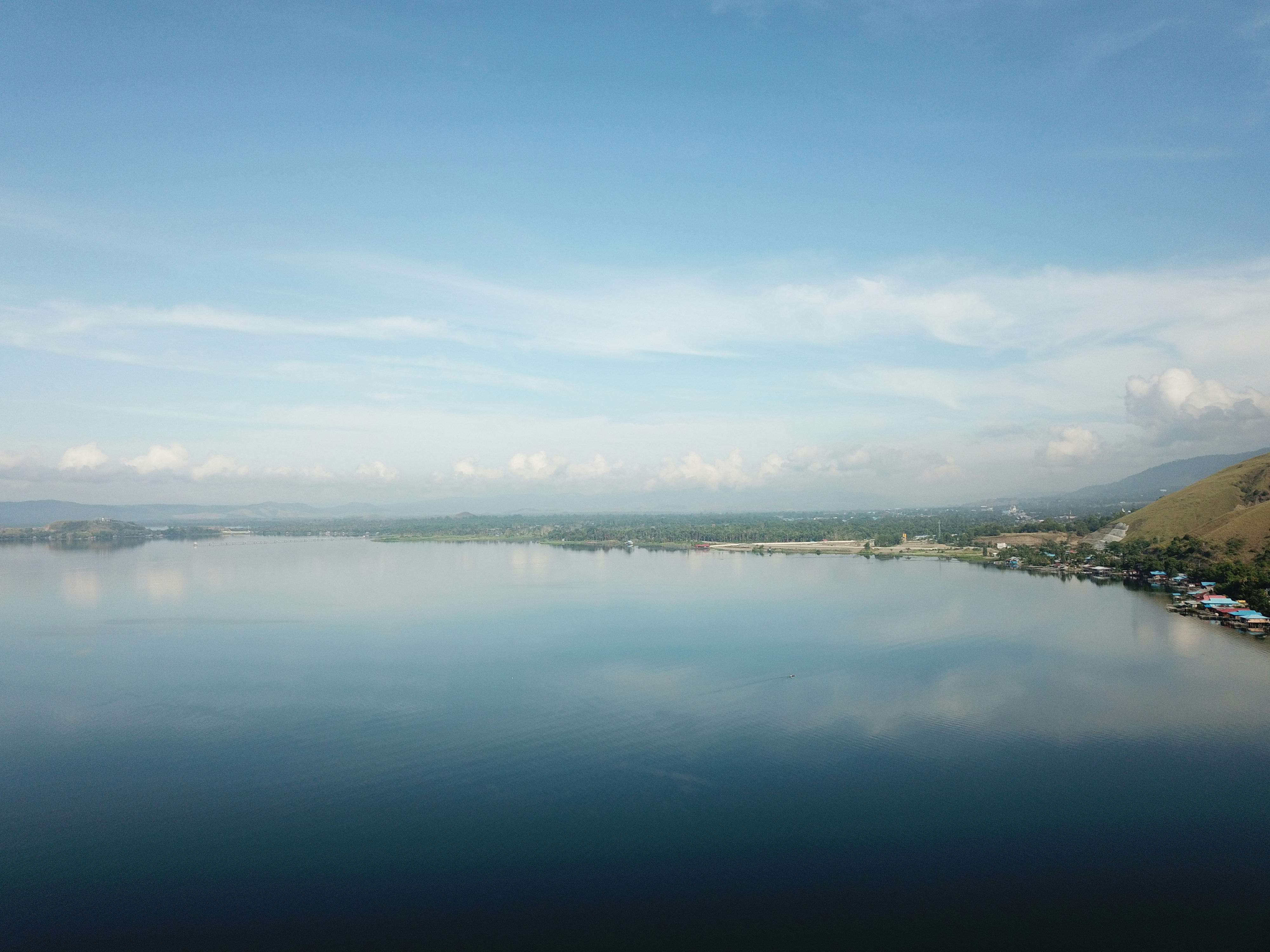 Expansive calm lake reflecting the blue sky with distant shoreline and mountains.