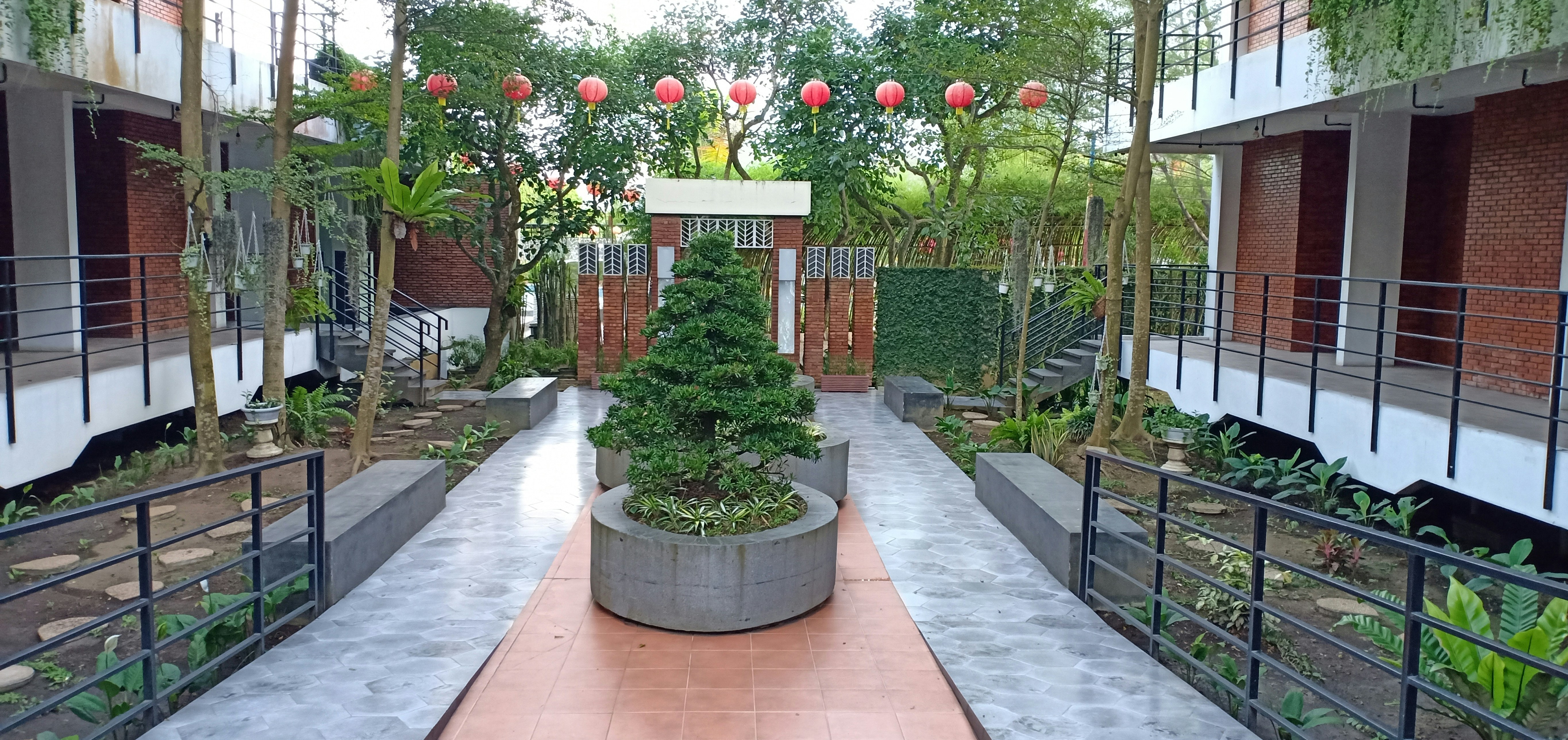 A tranquil courtyard featuring a central garden surrounded by modern architecture, enhanced by decorative lanterns above. The design promotes a peaceful atmosphere.