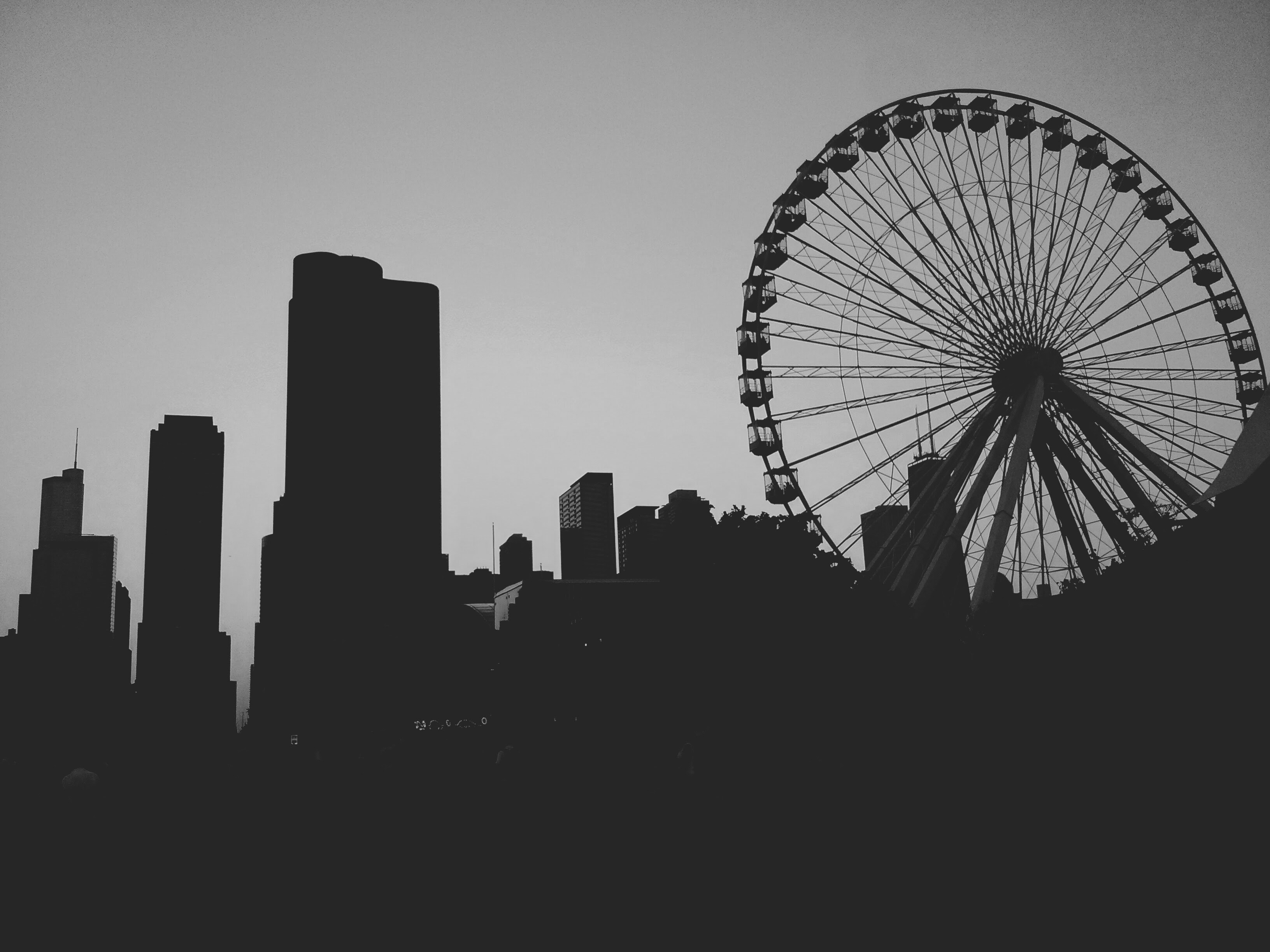Silhouette of a city skyline with a large Ferris wheel on the right against a gray sky.