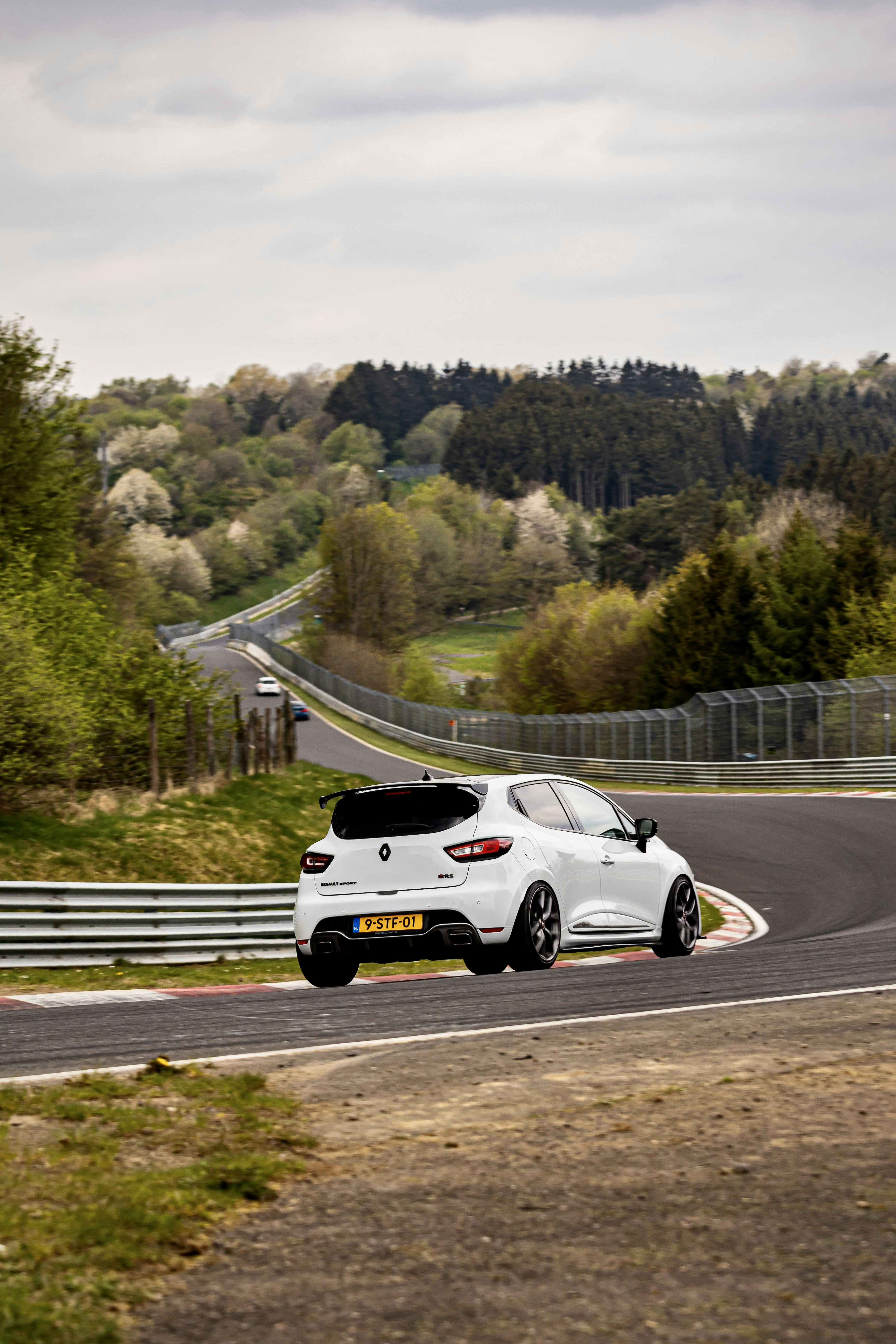 White hatchback carving a serpentine curve through a forested circuit