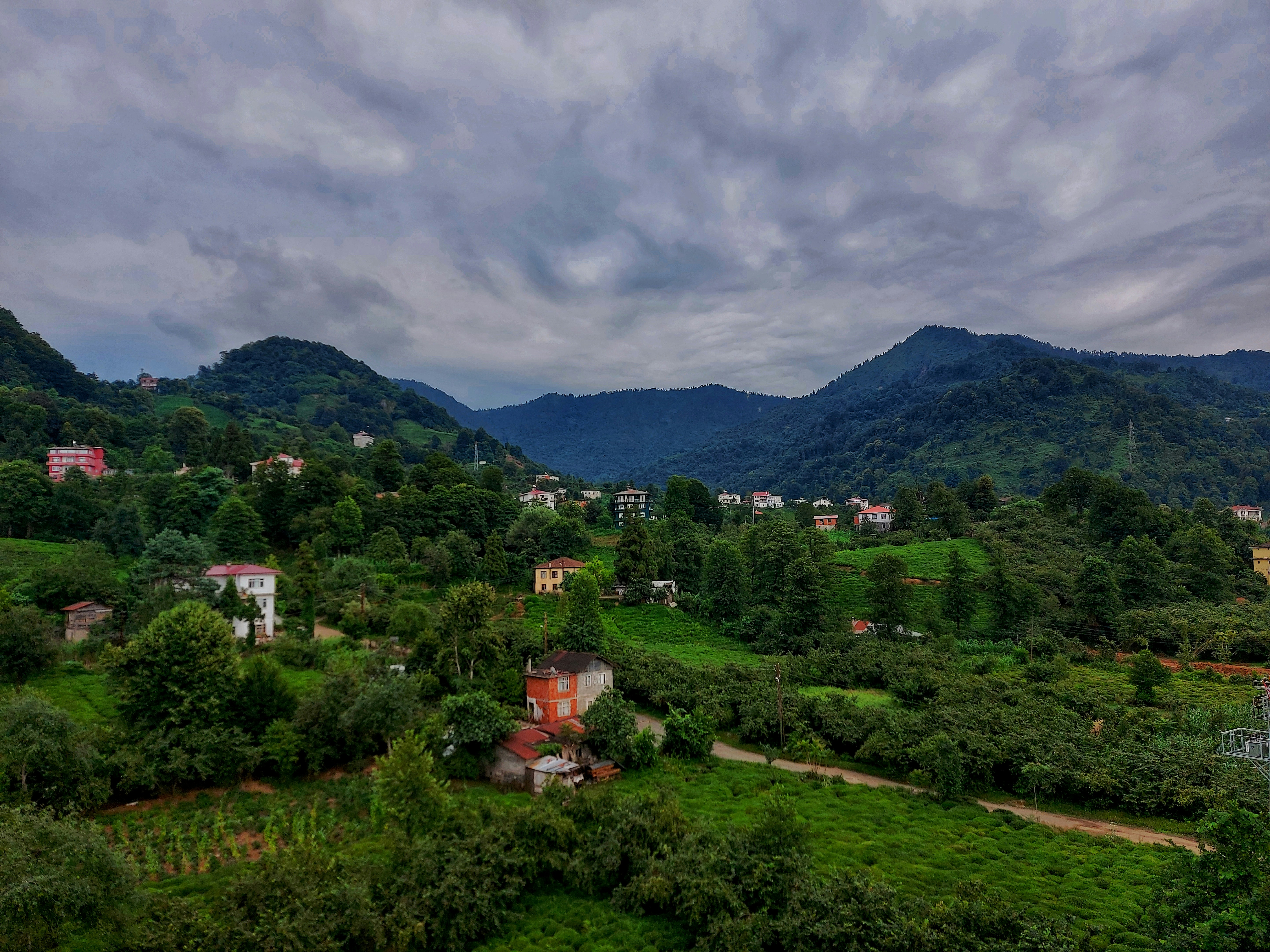 A tranquil landscape showcasing a blend of lush greenery and scattered homes nestled among the hills under a cloudy sky.