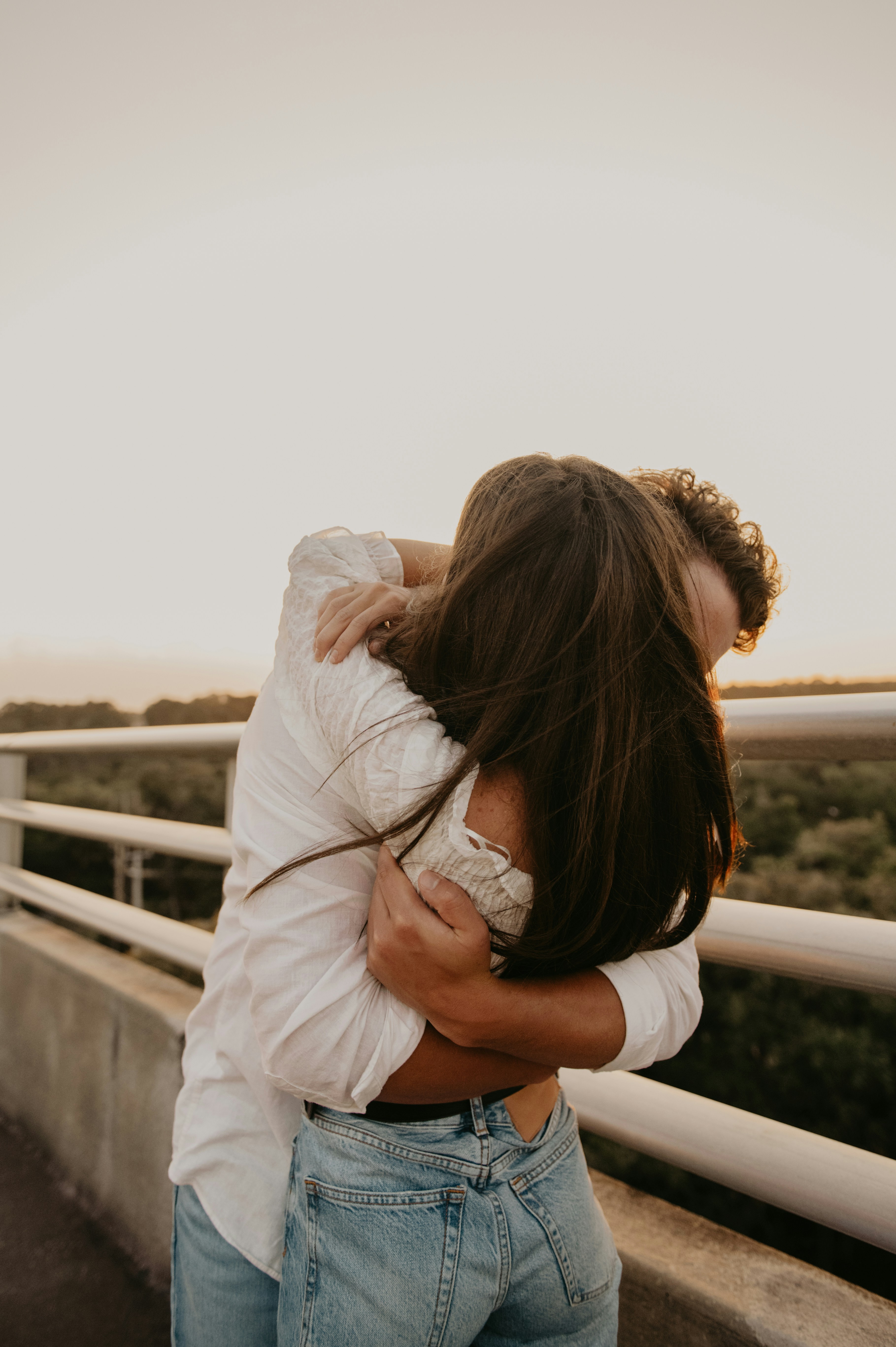 Couple sharing a warm embrace on a bridge during sunset, capturing a moment of intimacy and love.