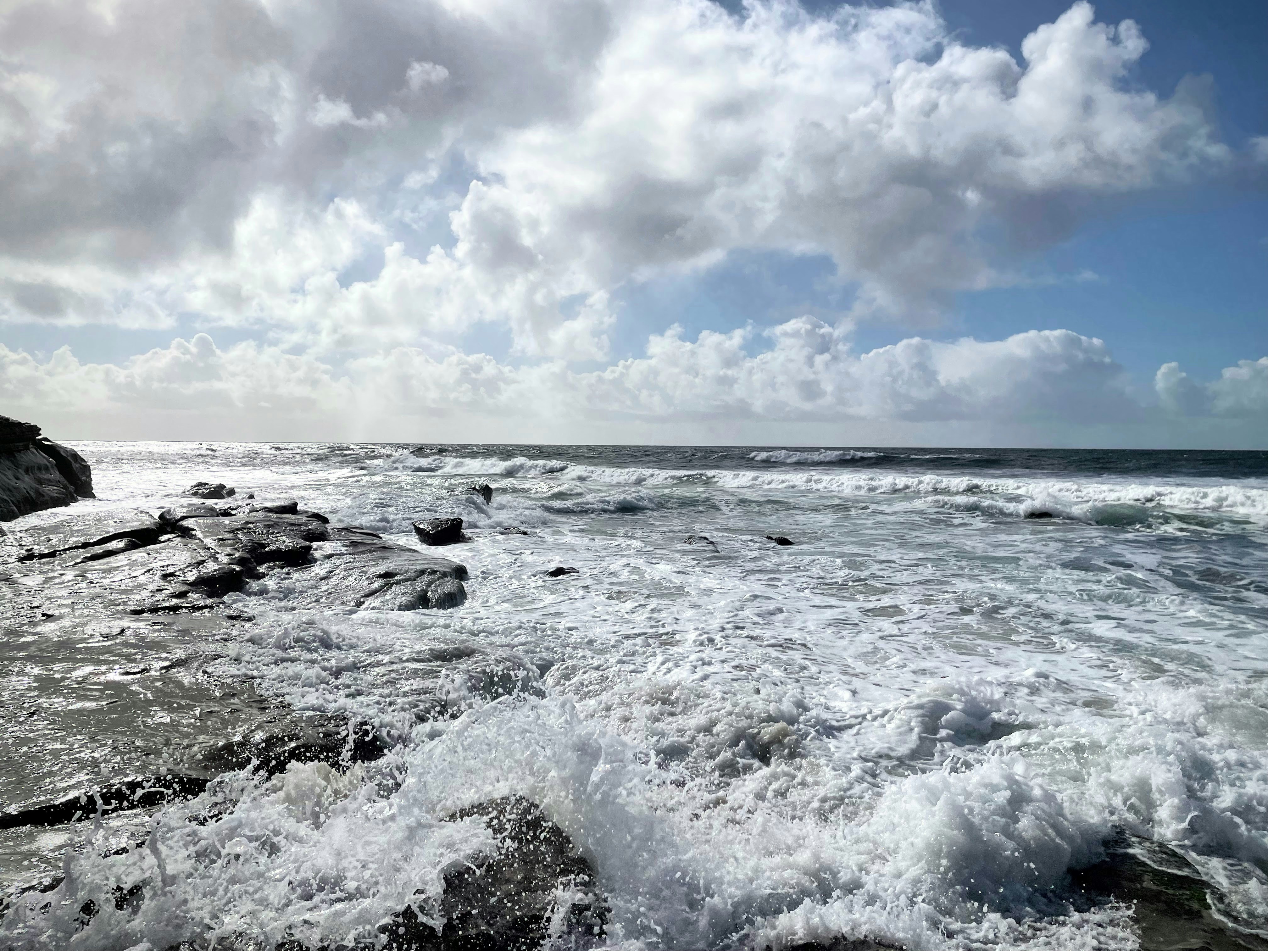 Waves crashing against rocky shoreline under a cloudy sky.