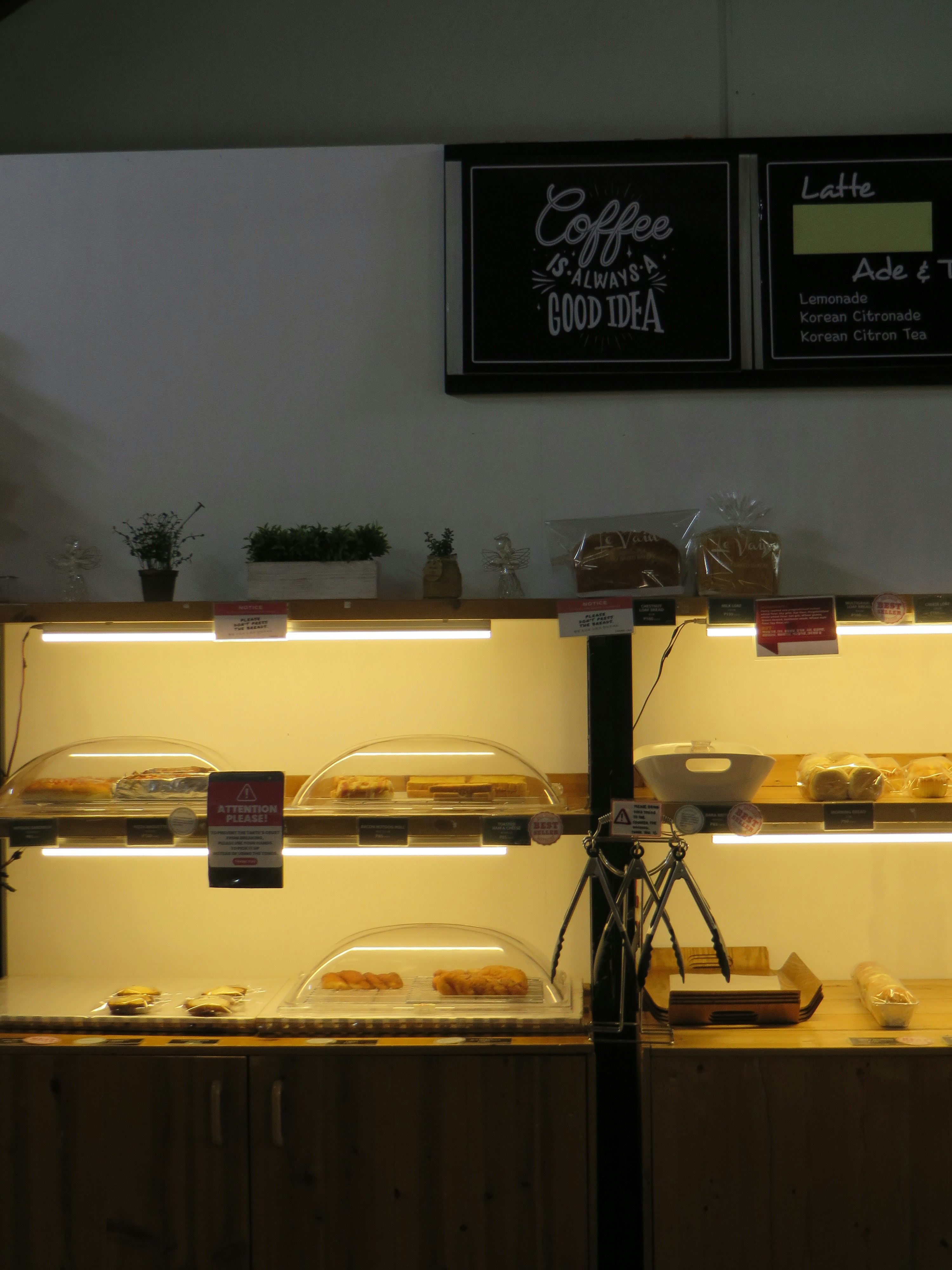 Display of assorted pastries and desserts under glass domes in a cozy café setting. A chalkboard sign promotes coffee and latte options.