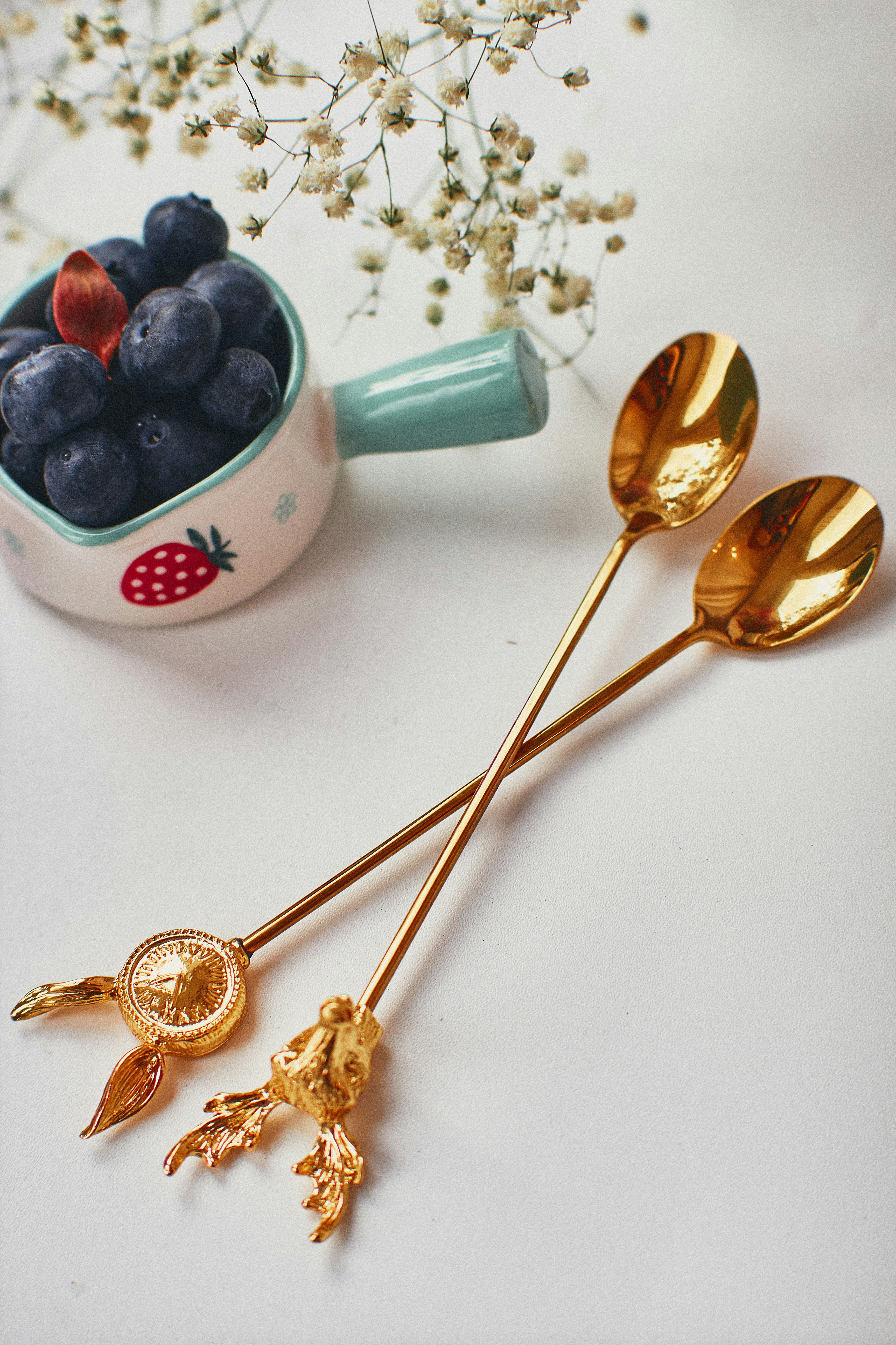 Blueberries in a Mint Mug, with Crossed Golden Spoons on White Studio Surface