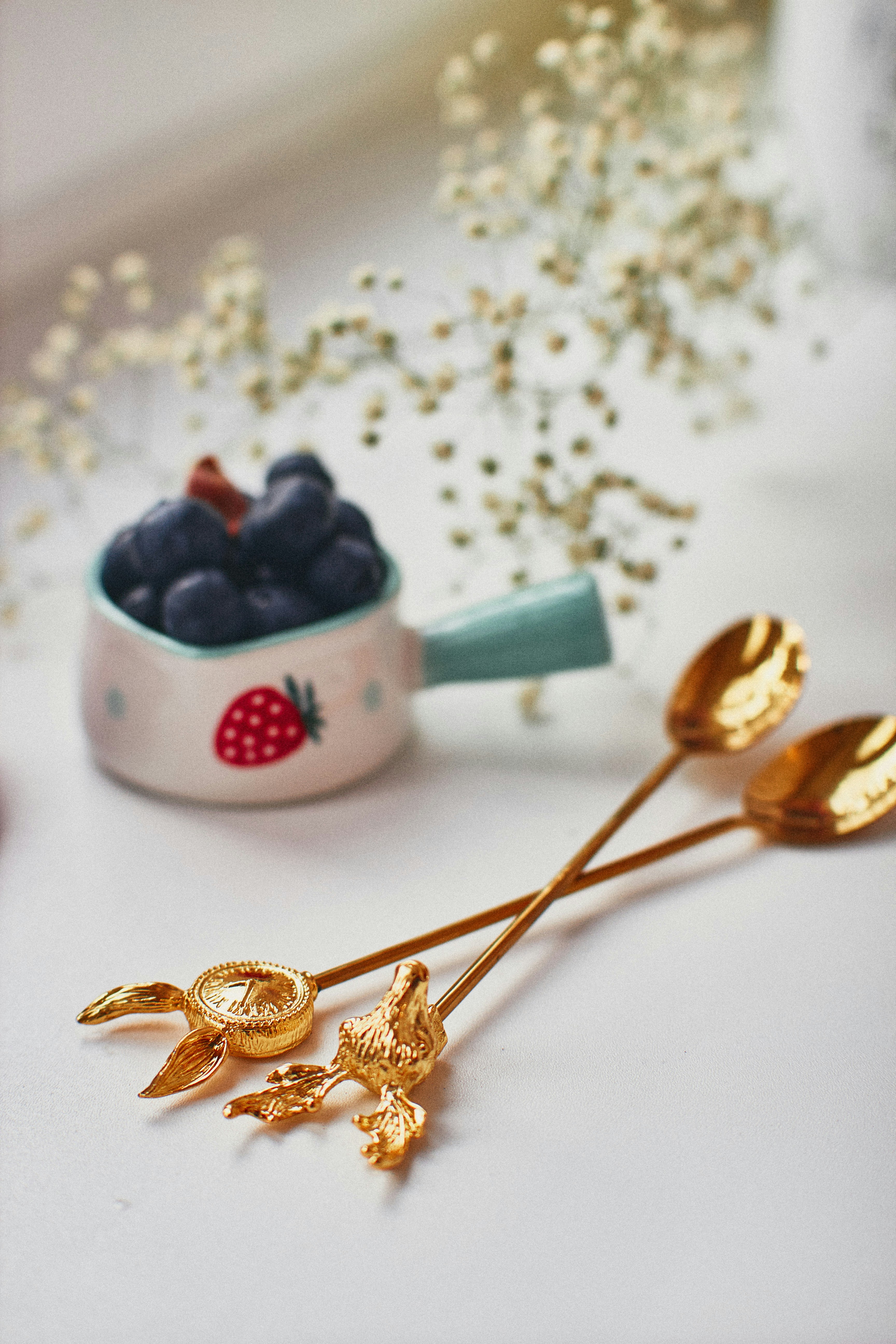 Gold-Sheathed Spoons Crisscross a Quiet White Still Life with Blueberries