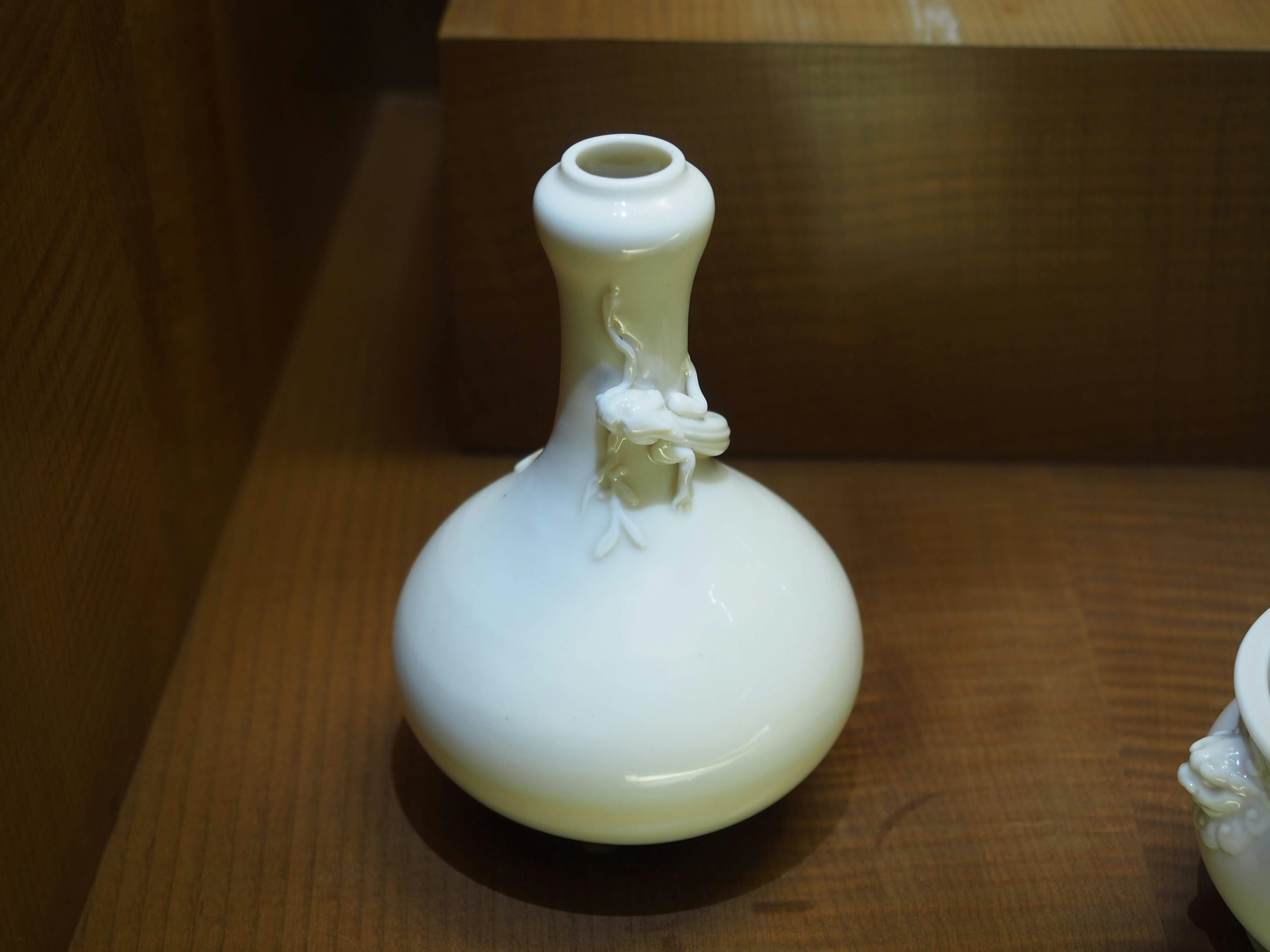 Intricately designed white porcelain vase featuring delicate floral reliefs, set against a warm wooden backdrop.