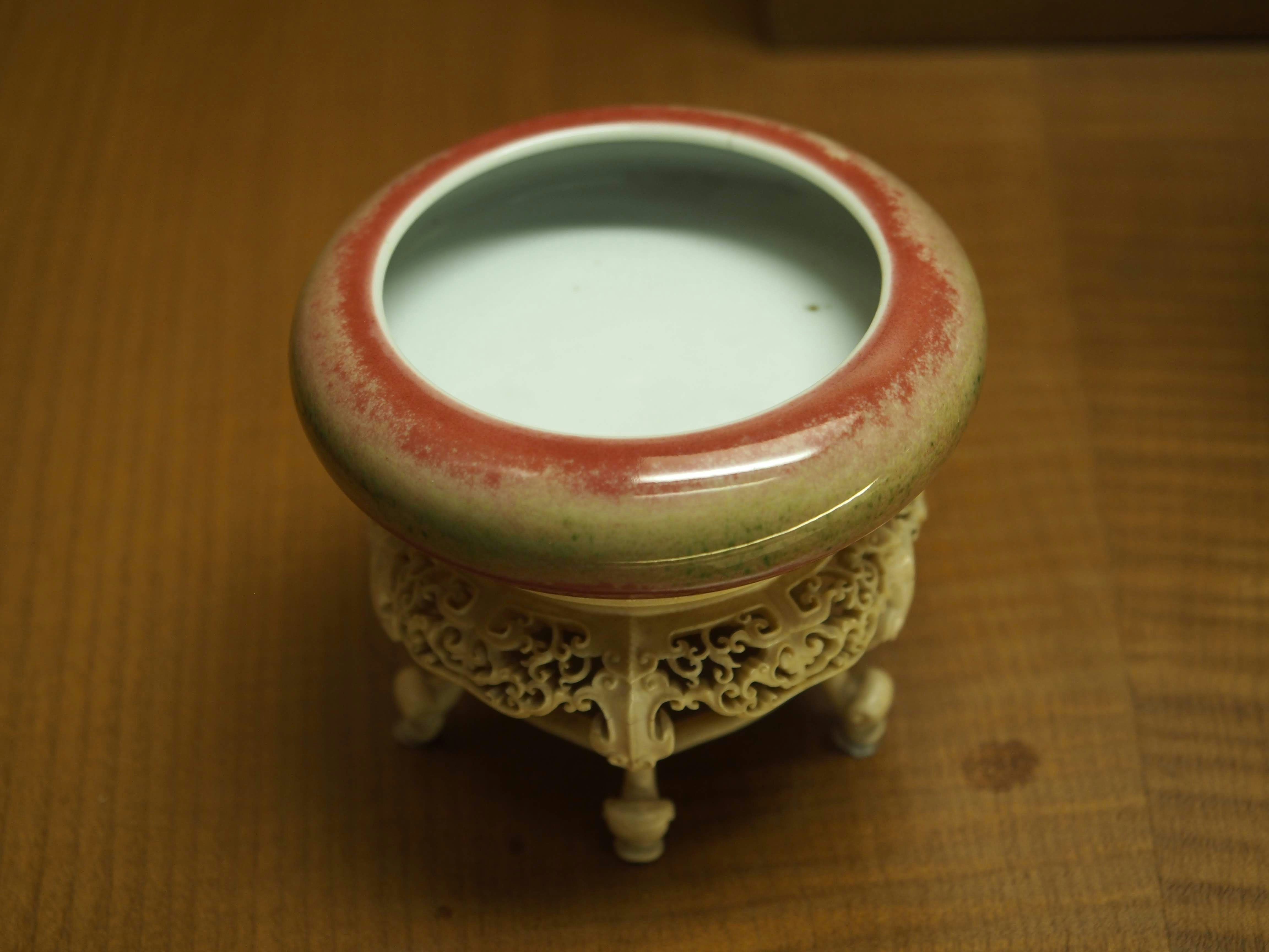 Scarlet-rimmed ceramic bowl perched on an ornate carved pedestal