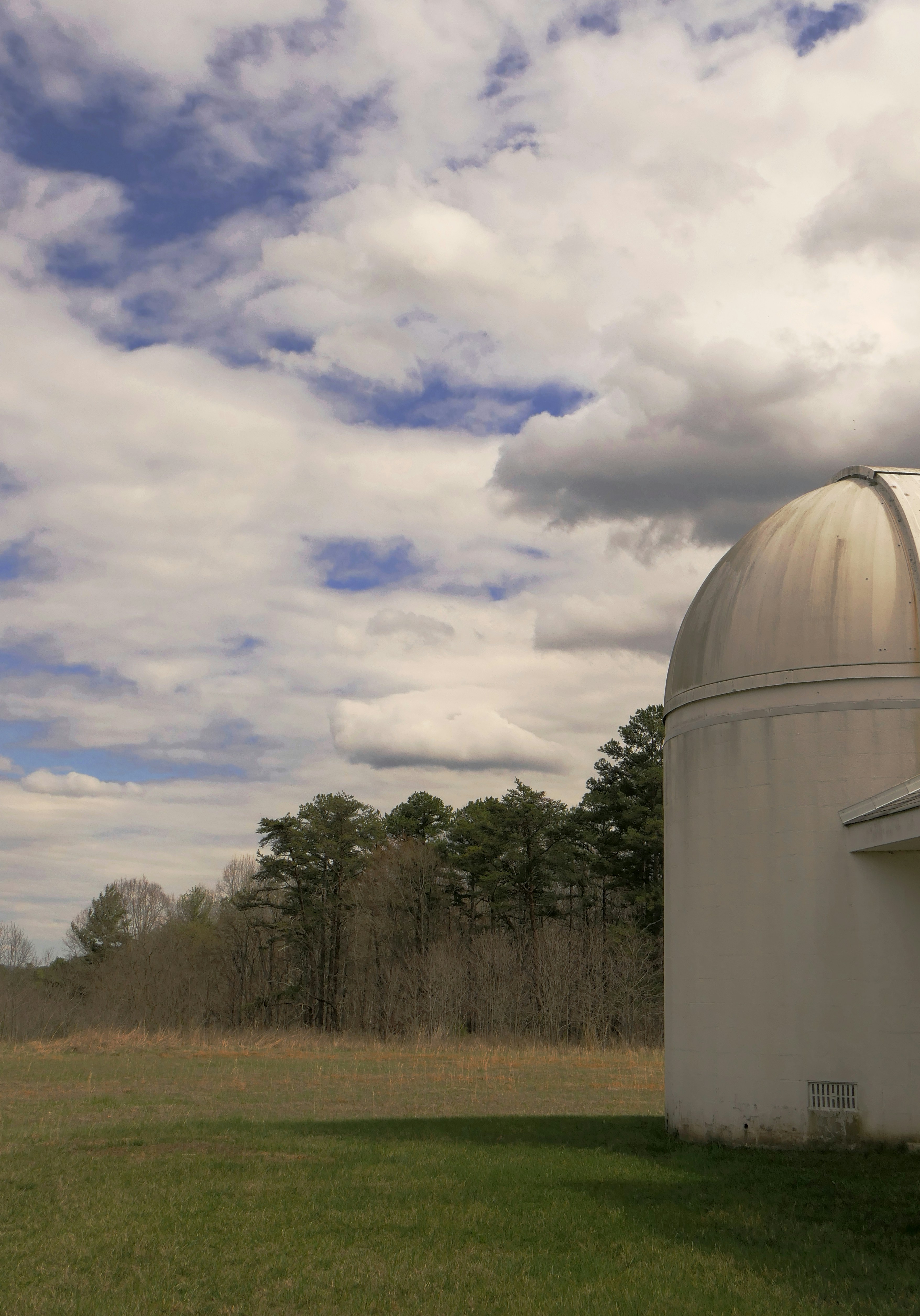 An observatory dome stands resilient against a backdrop of dynamic clouds and distant trees, hinting at the wonders of the universe beyond.