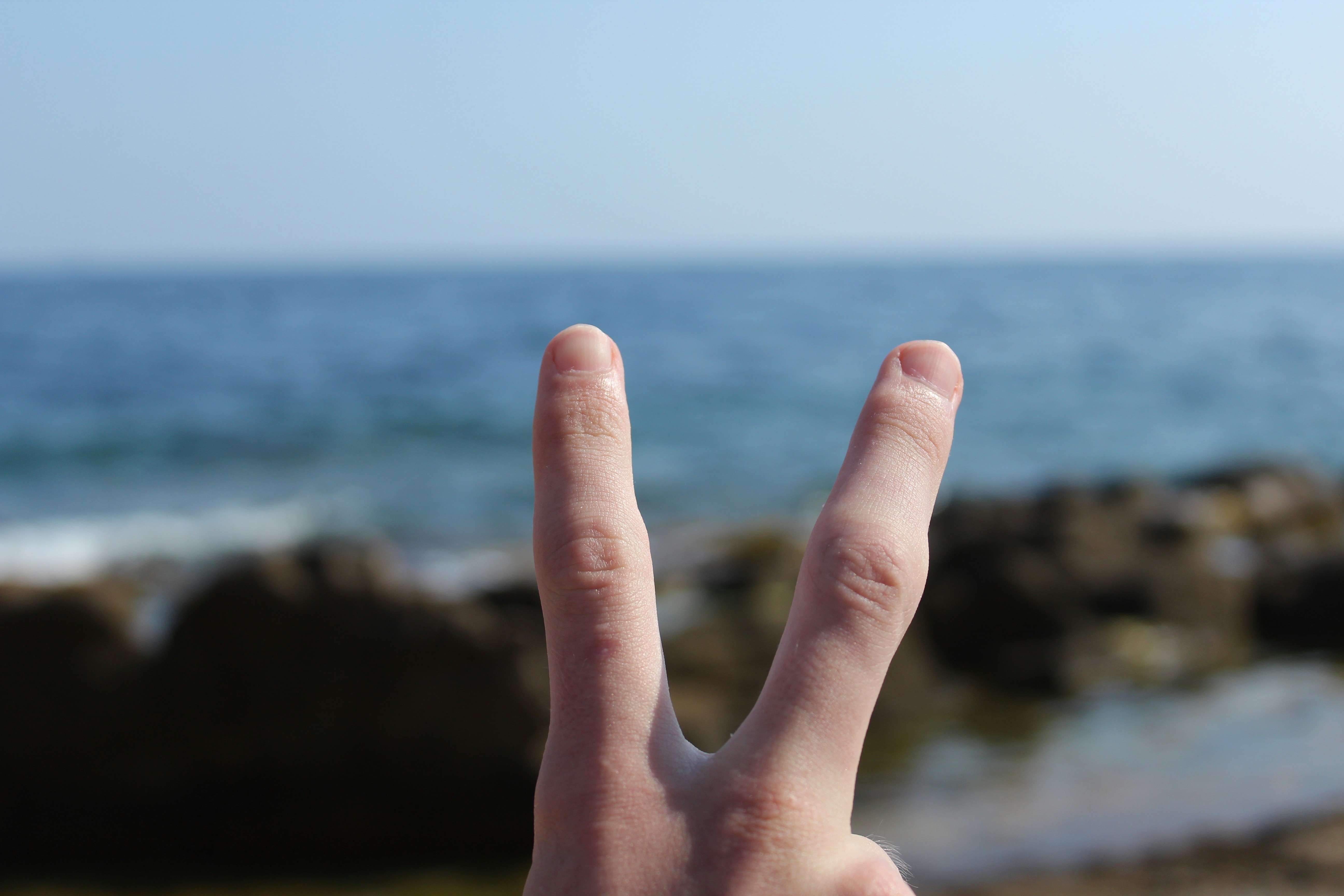 Hand forming a peace sign in front of a serene ocean backdrop, capturing a moment of tranquility and connection with nature.
