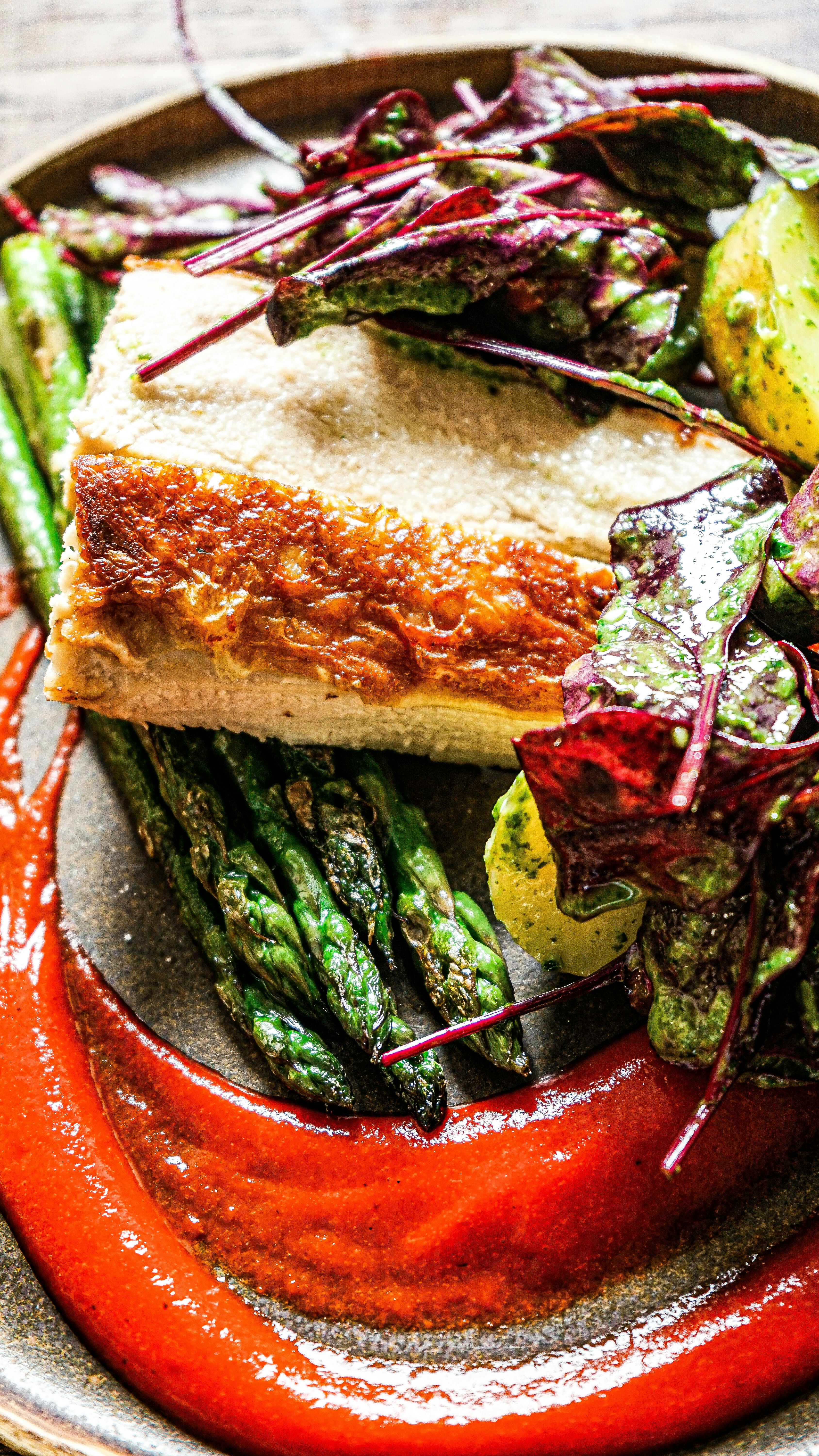 A beautifully plated dish featuring crispy skin fish atop fresh asparagus and vibrant greens, drizzled with a rich sauce.