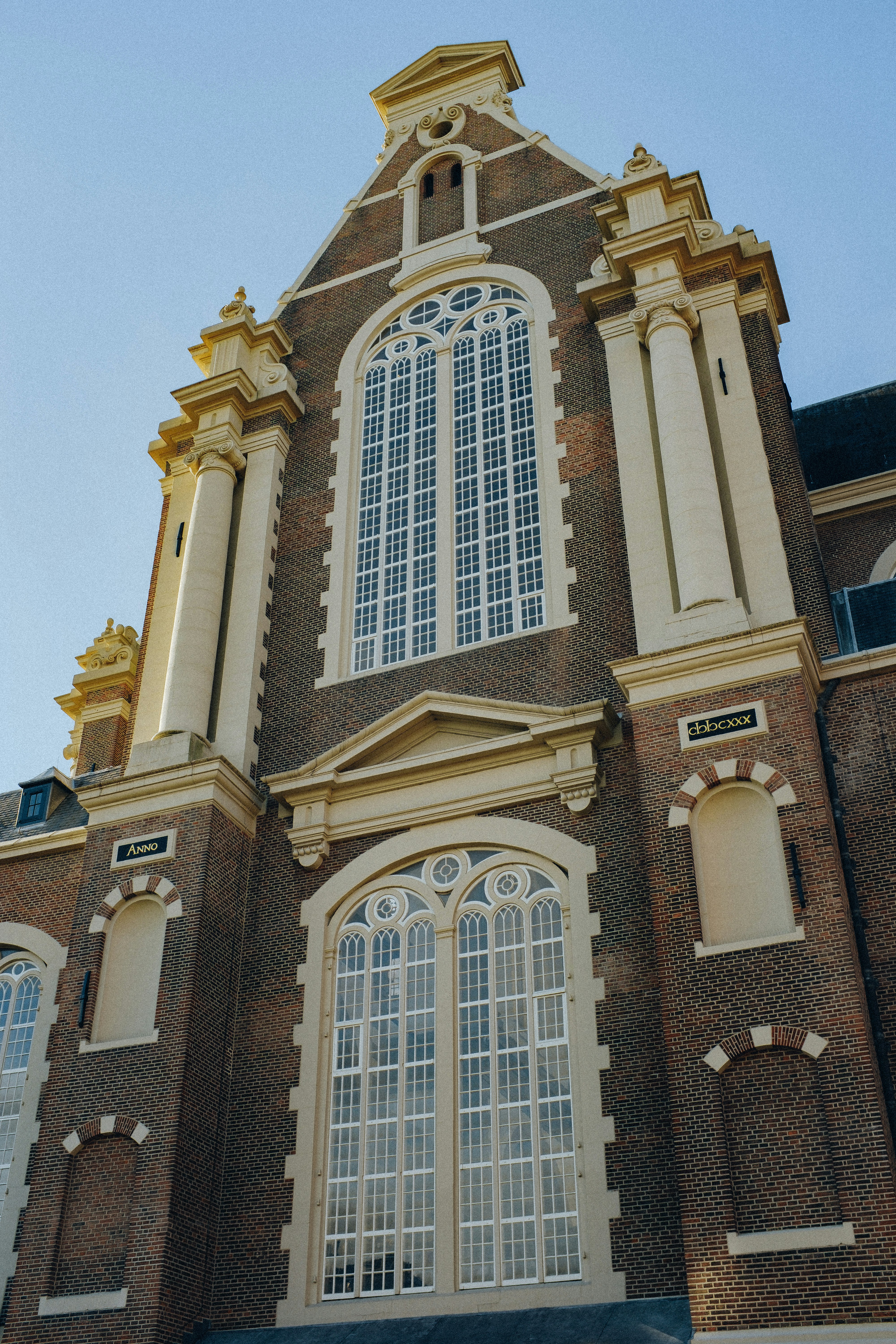 Imposing brick facade of a historic building featuring intricate windows and decorative elements. The sunlight highlights the architectural details beautifully.