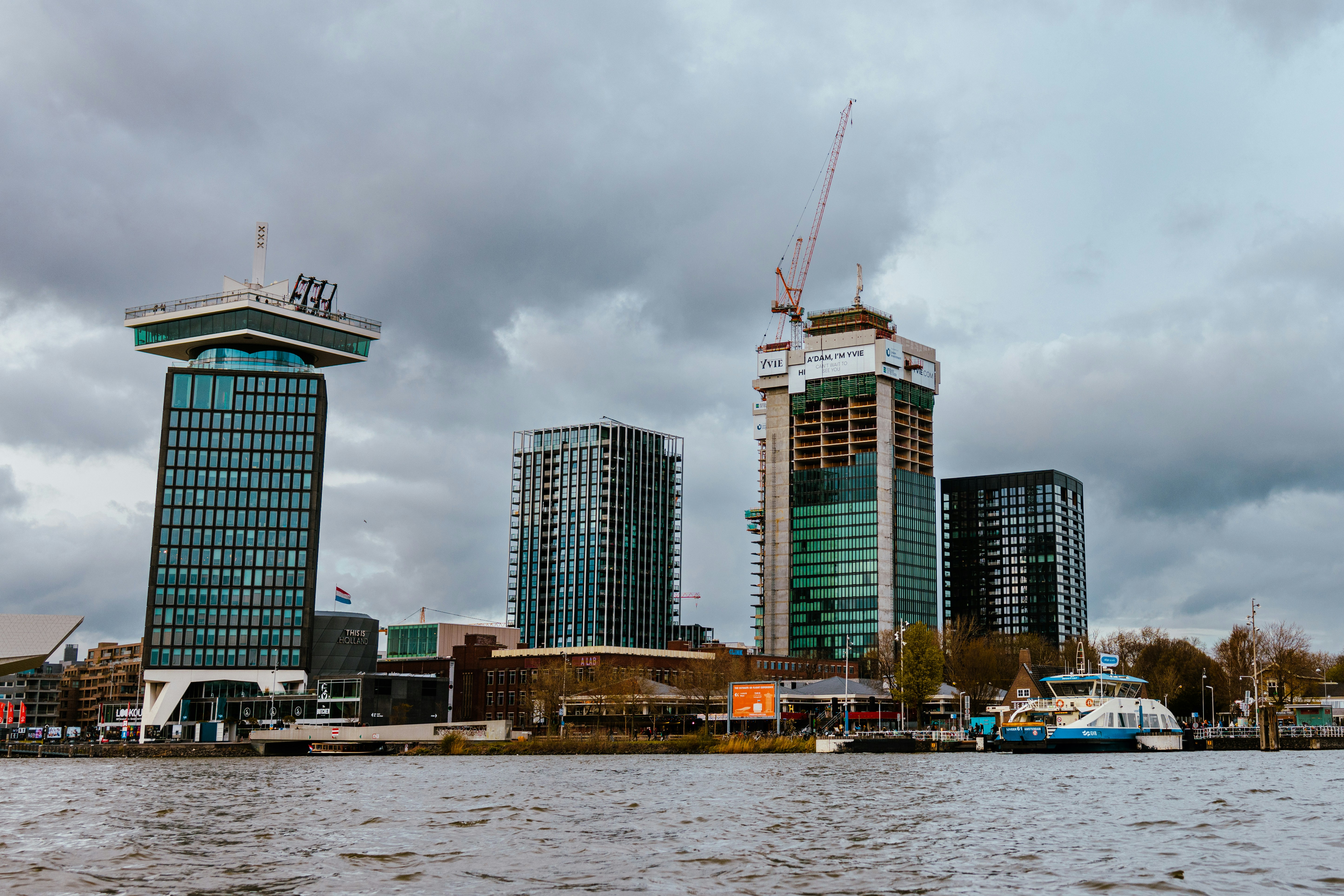 Glass Monoliths by the Water: Cranes and Cloud-Heavy Skies Over a Riverfront