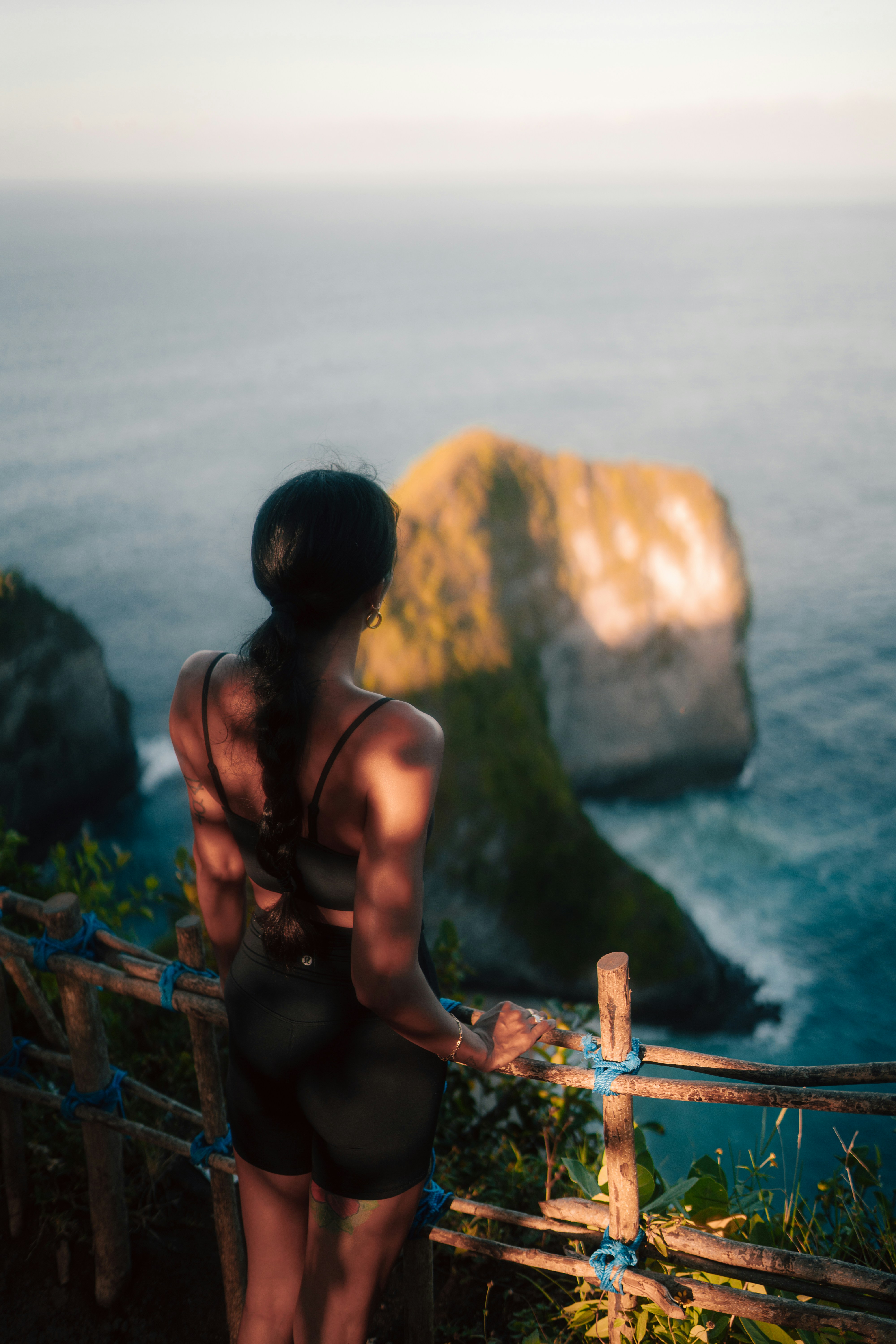 Ledge of Quiet Light: a solitary figure framed by weathered rails overlooking a sunlit sea stack