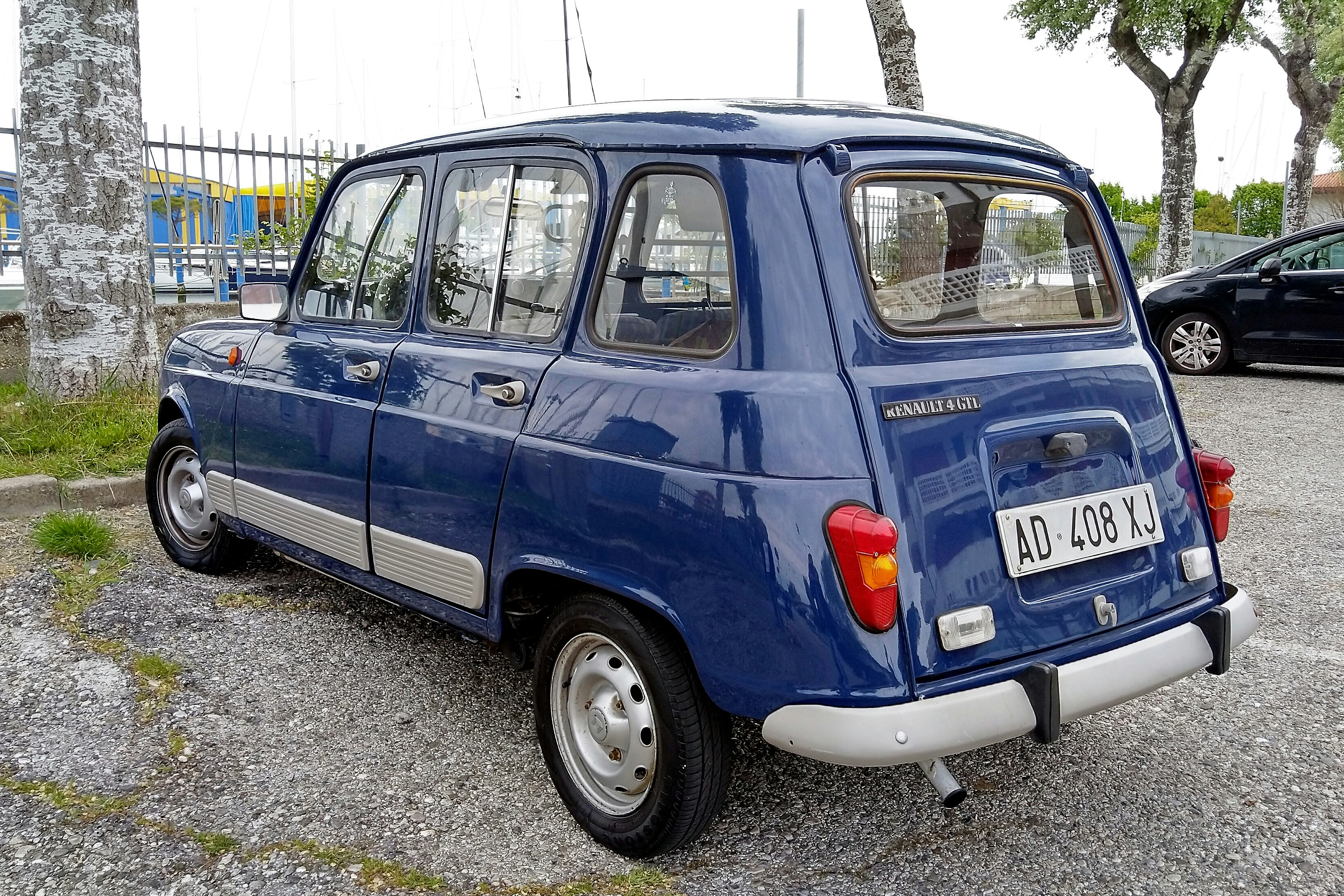 Classic blue Renault 4 parked in a gravel lot, showcasing its vintage design and character against a backdrop of trees and distant boats.