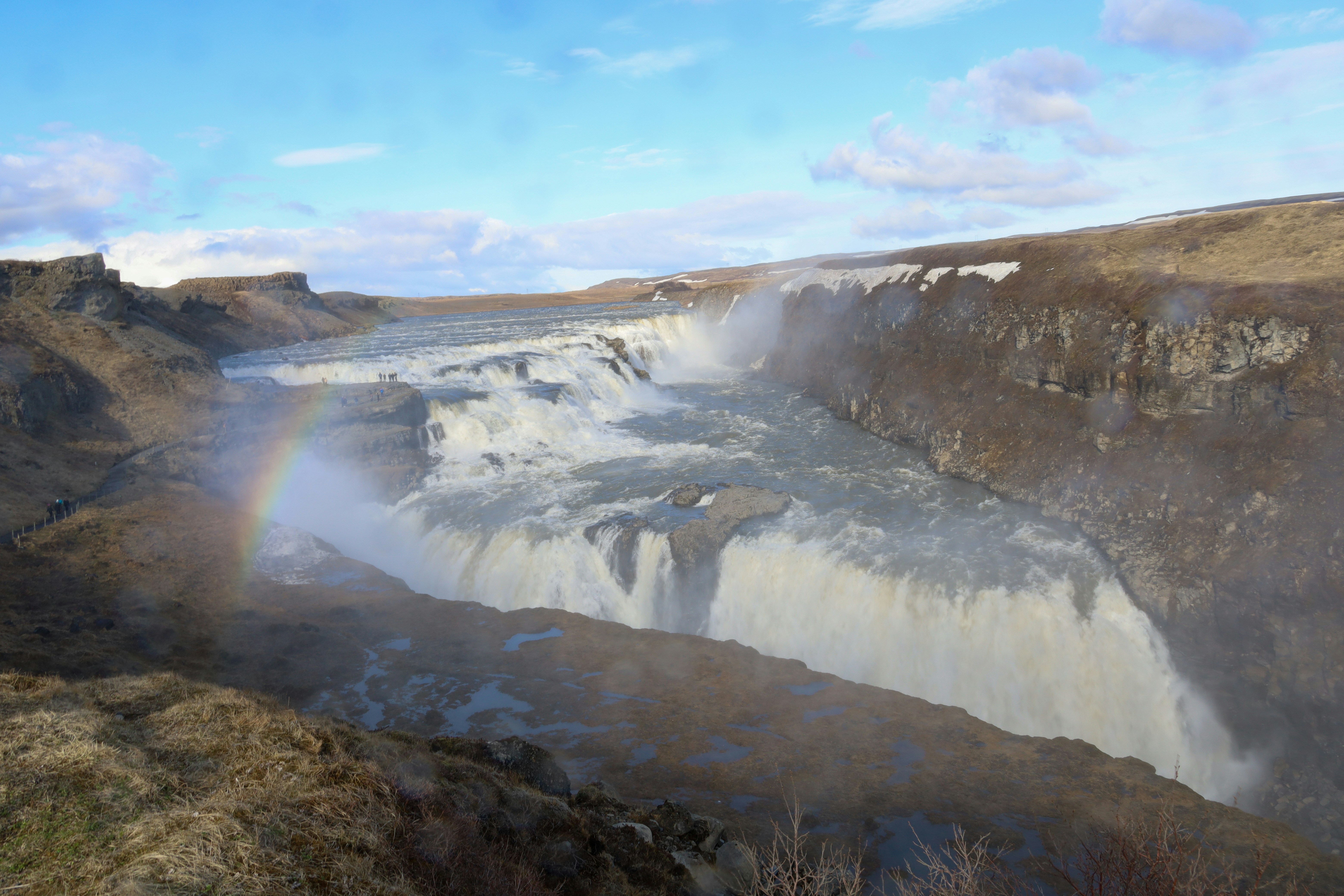 Powerful waterfall cascading over rocky cliffs, with a faint rainbow arching through the mist. A serene landscape captures the essence of nature's force.