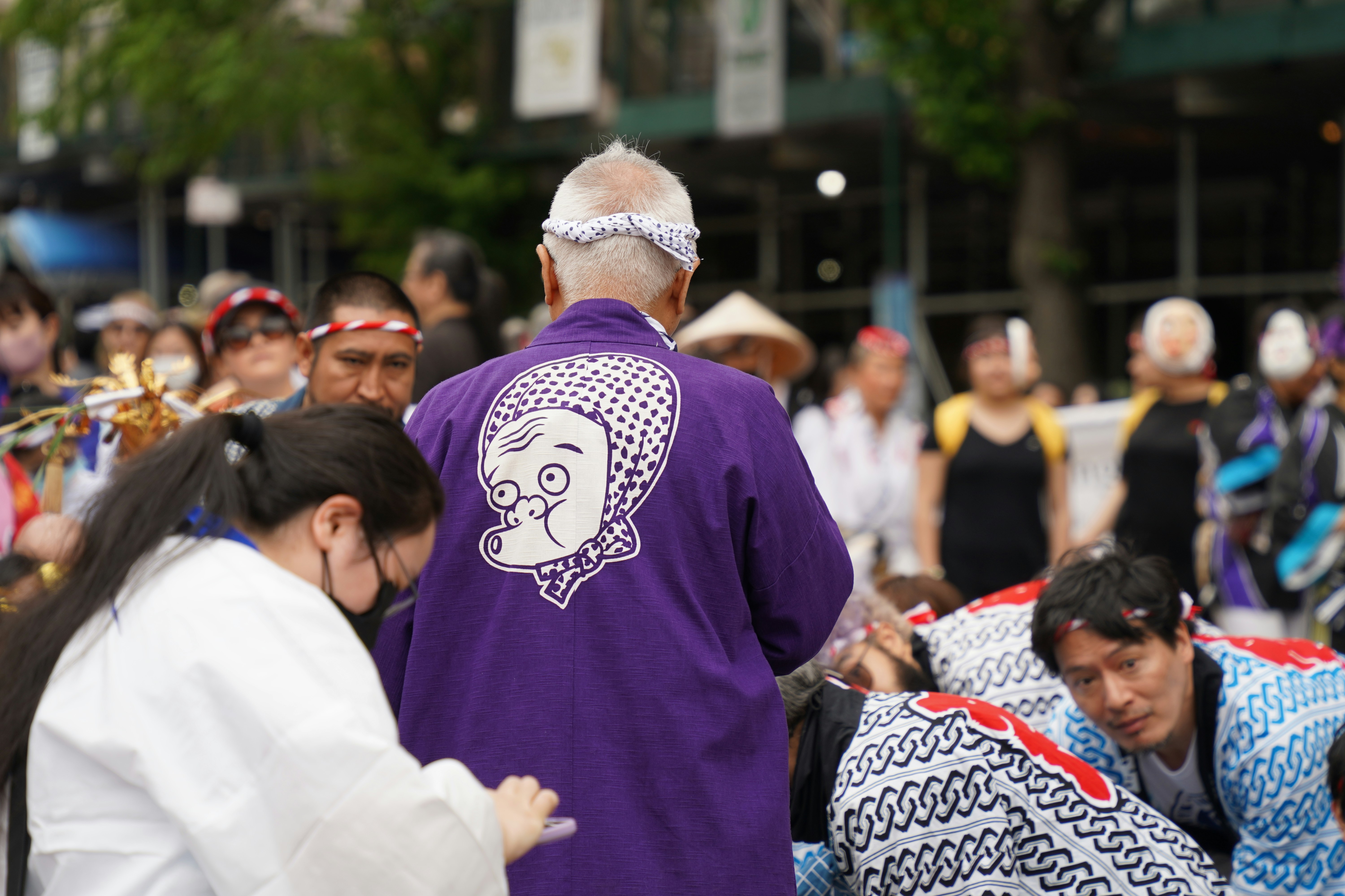 Back View: The Purple-Robed Elder Amid a Lively Street Festival